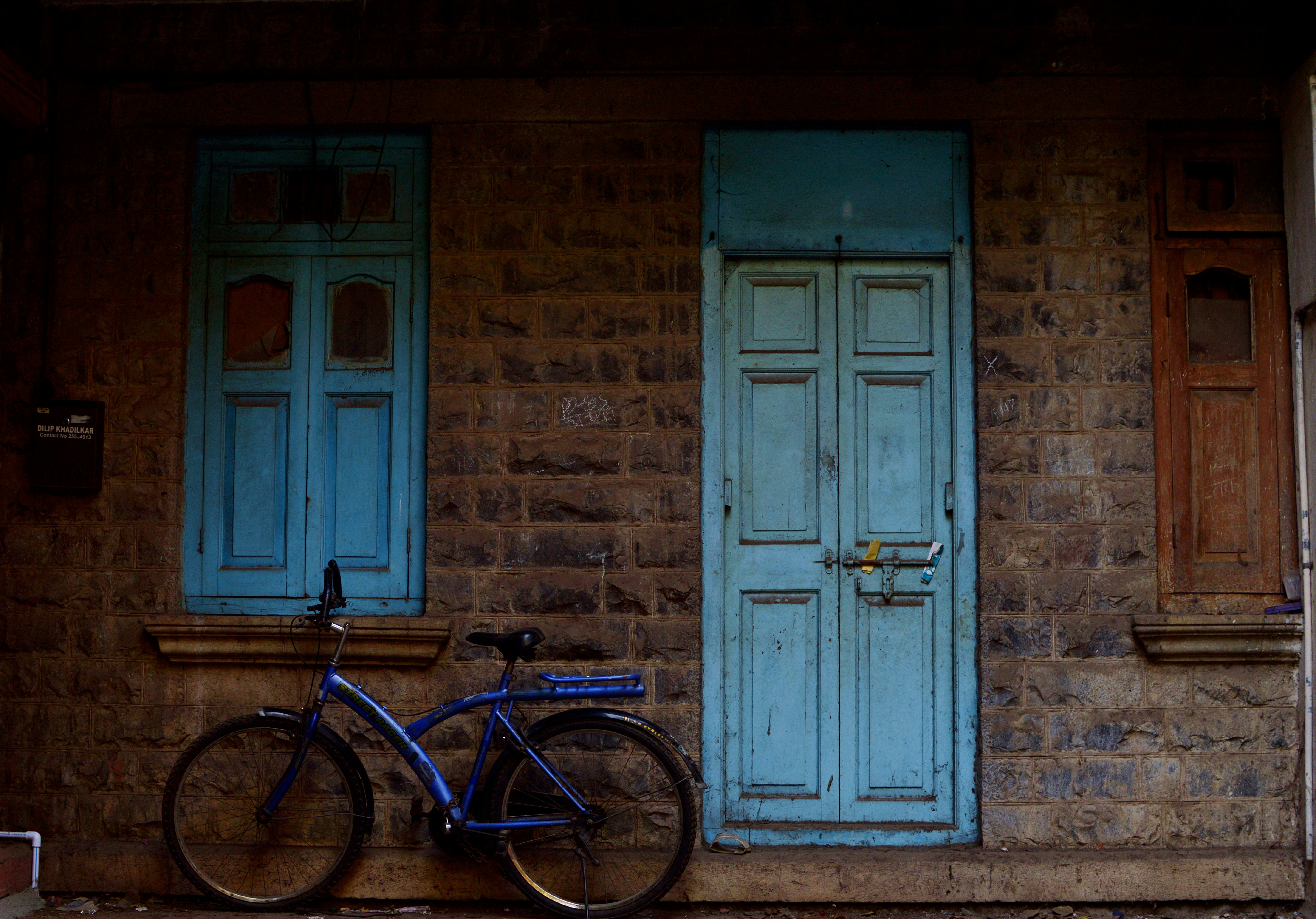 Vintage bicycle leaning against a rustic wall with blue doors and windows.