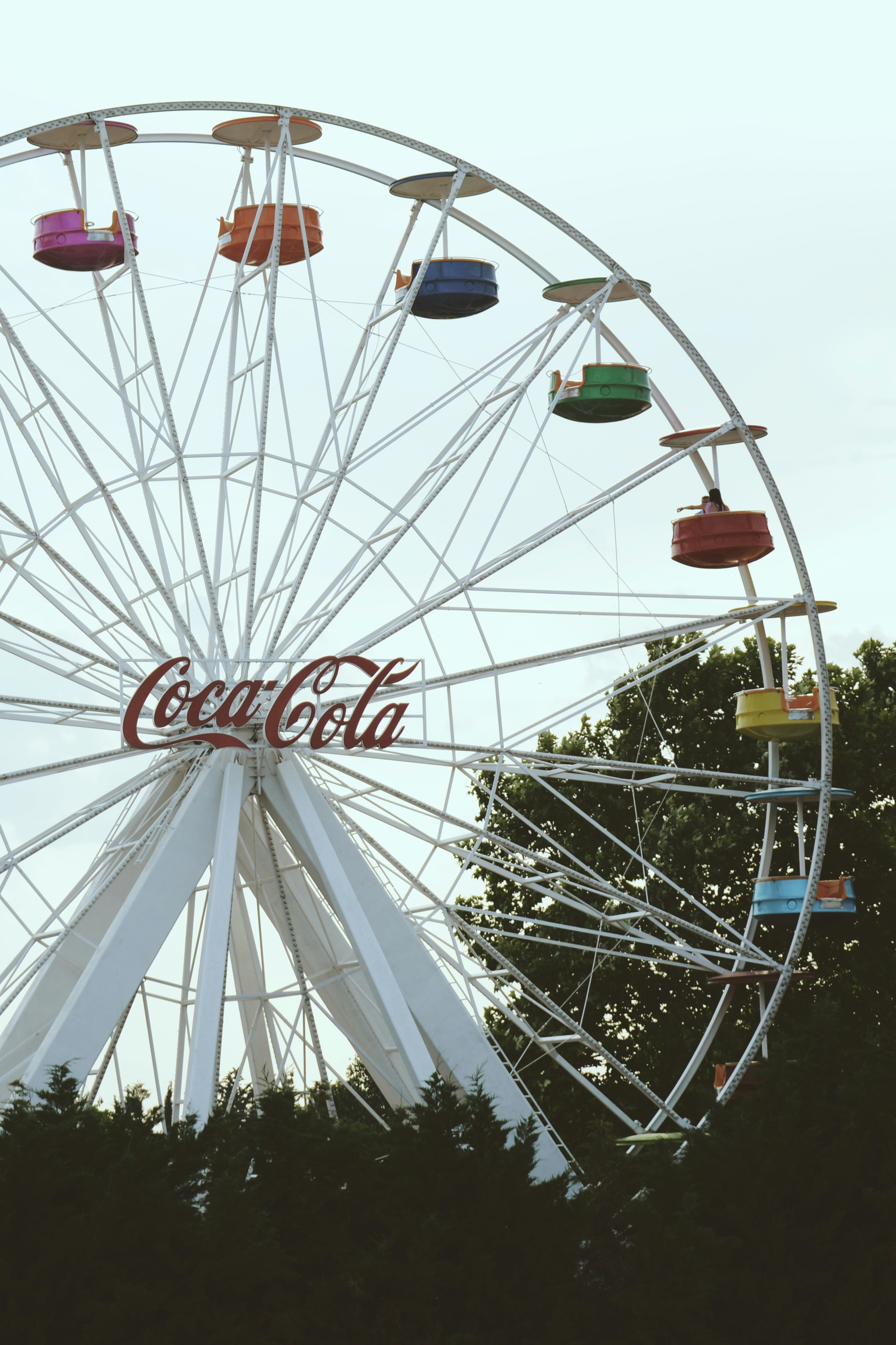 Ferris wheel adorned with vibrant gondolas and a prominent Coca-Cola logo, set against a soft sky backdrop.