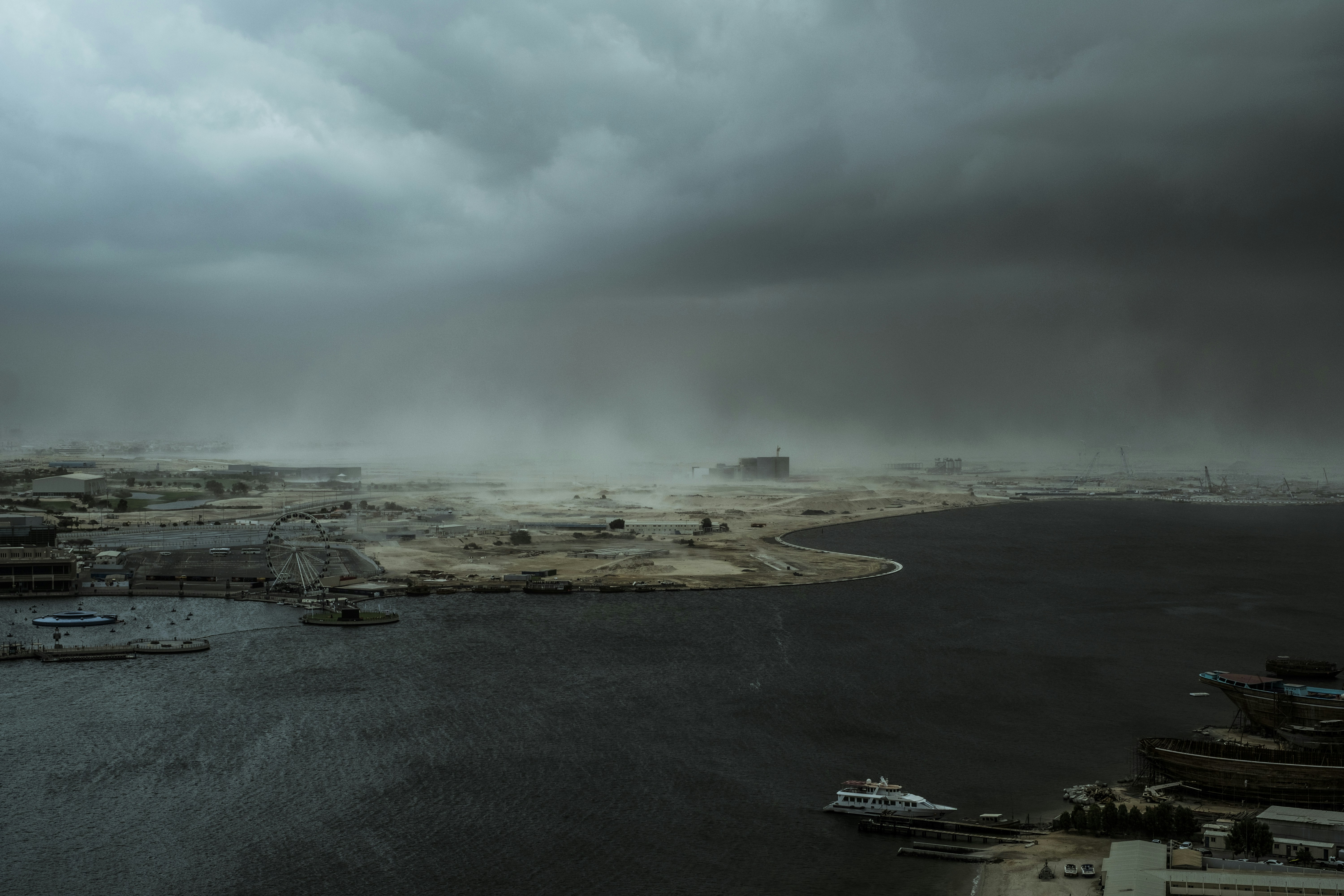 A dramatic view of a coastal landscape shrouded in dark clouds and mist, hinting at an impending storm. The turbulent waters reflect the ominous atmosphere.