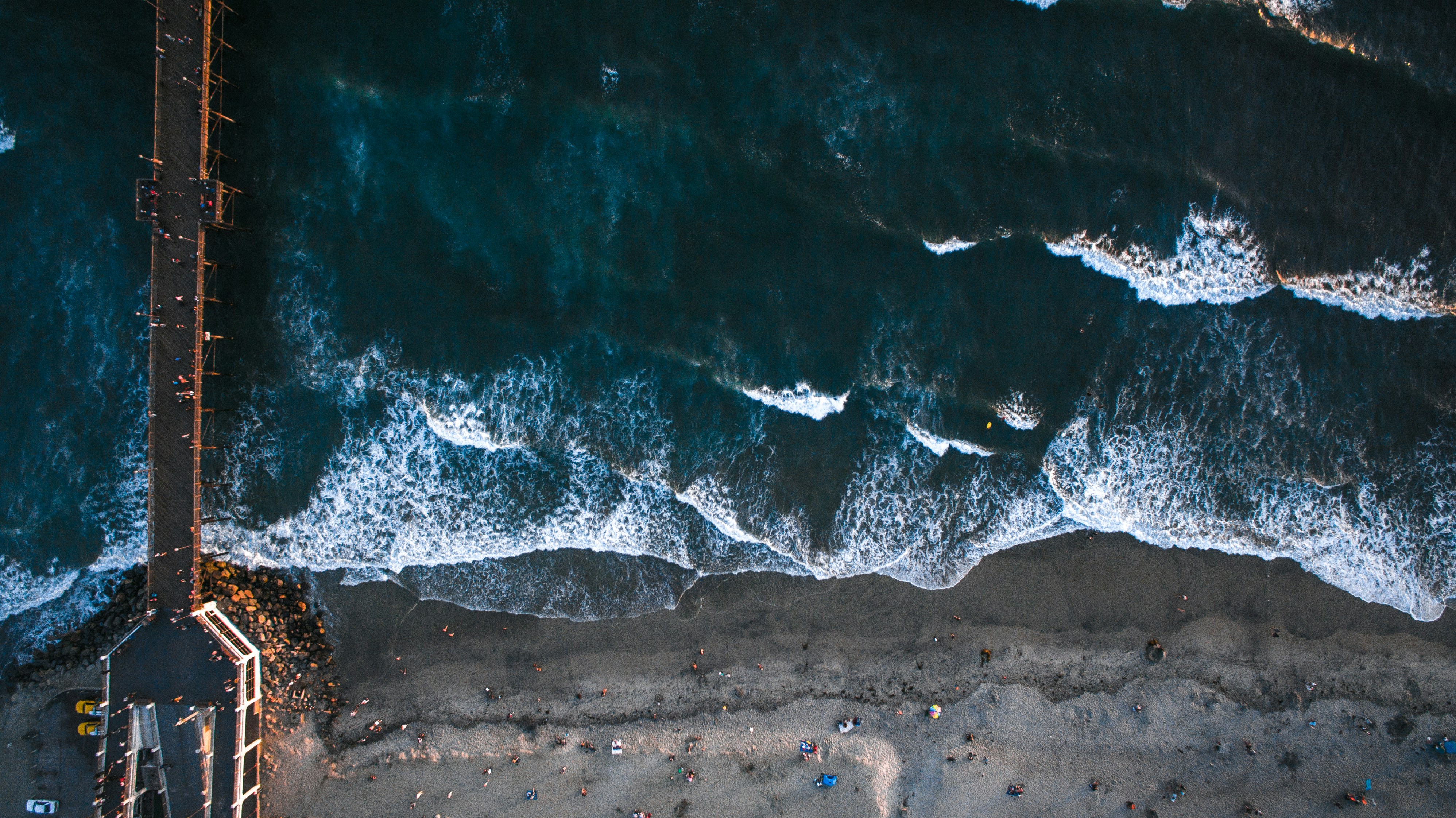 Aerial view of waves crashing against a beach near a pier.