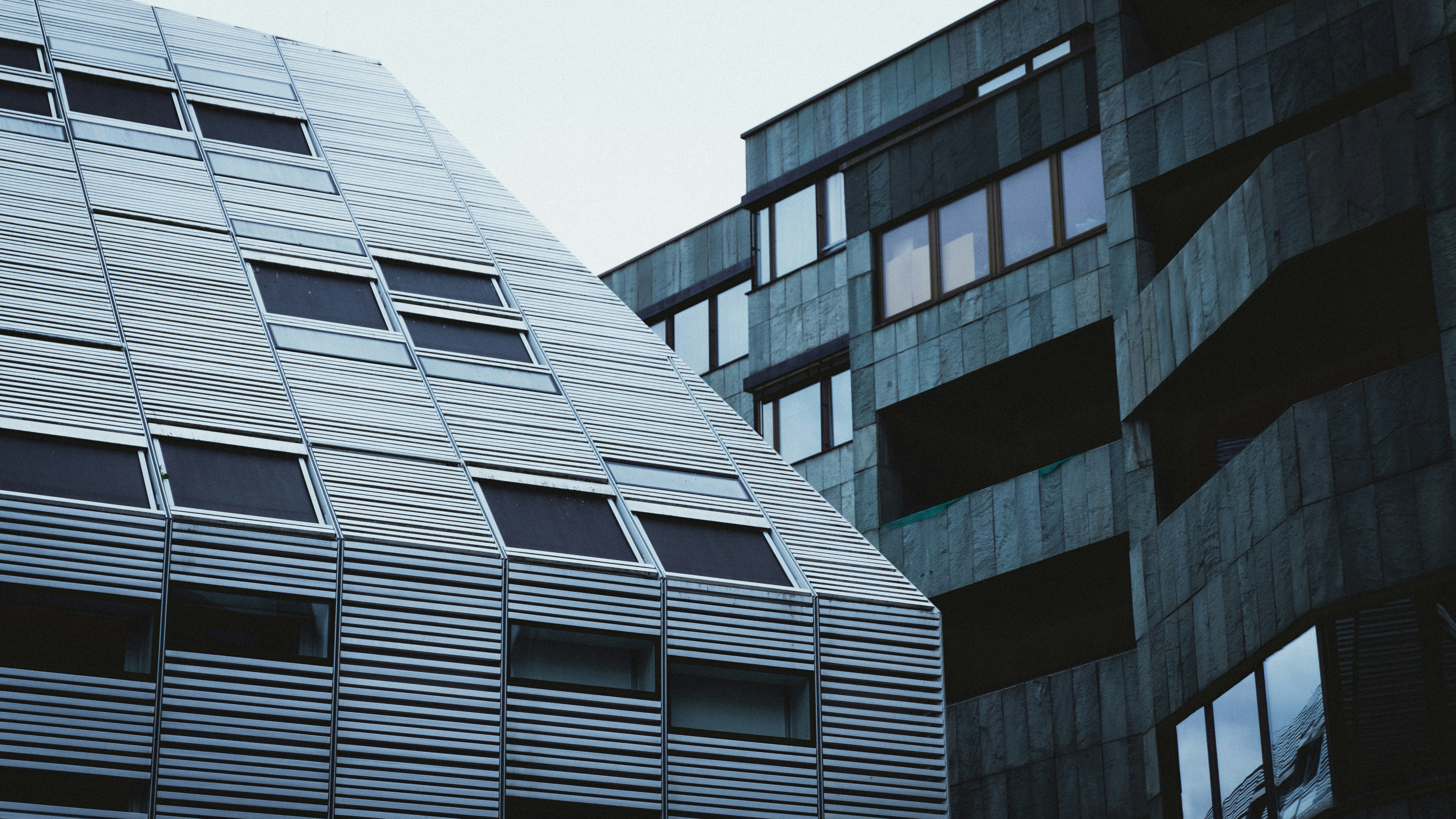 Modern buildings with intersecting angular surfaces and varied textures under a muted sky.