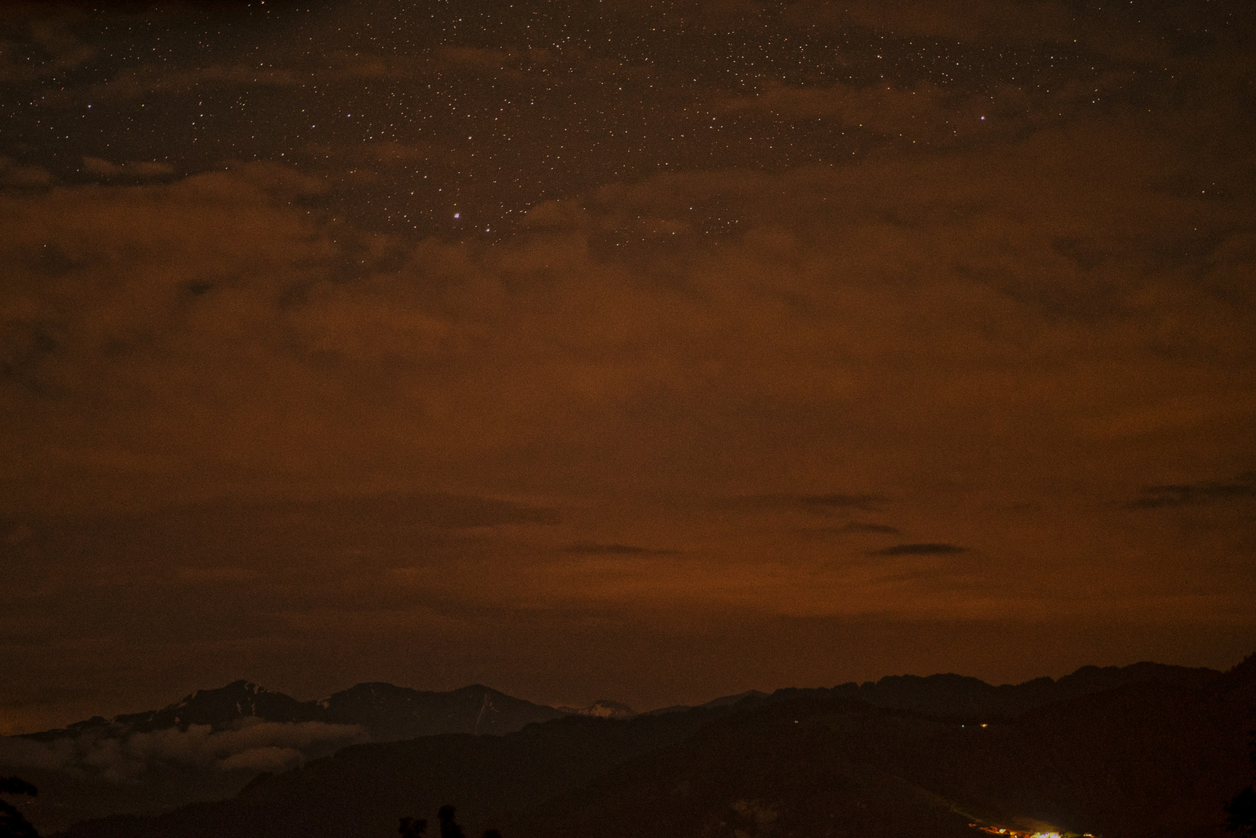A serene night landscape showcasing a starry sky over distant mountains, partially veiled by clouds. The soft glow of the horizon adds a mystical ambiance.