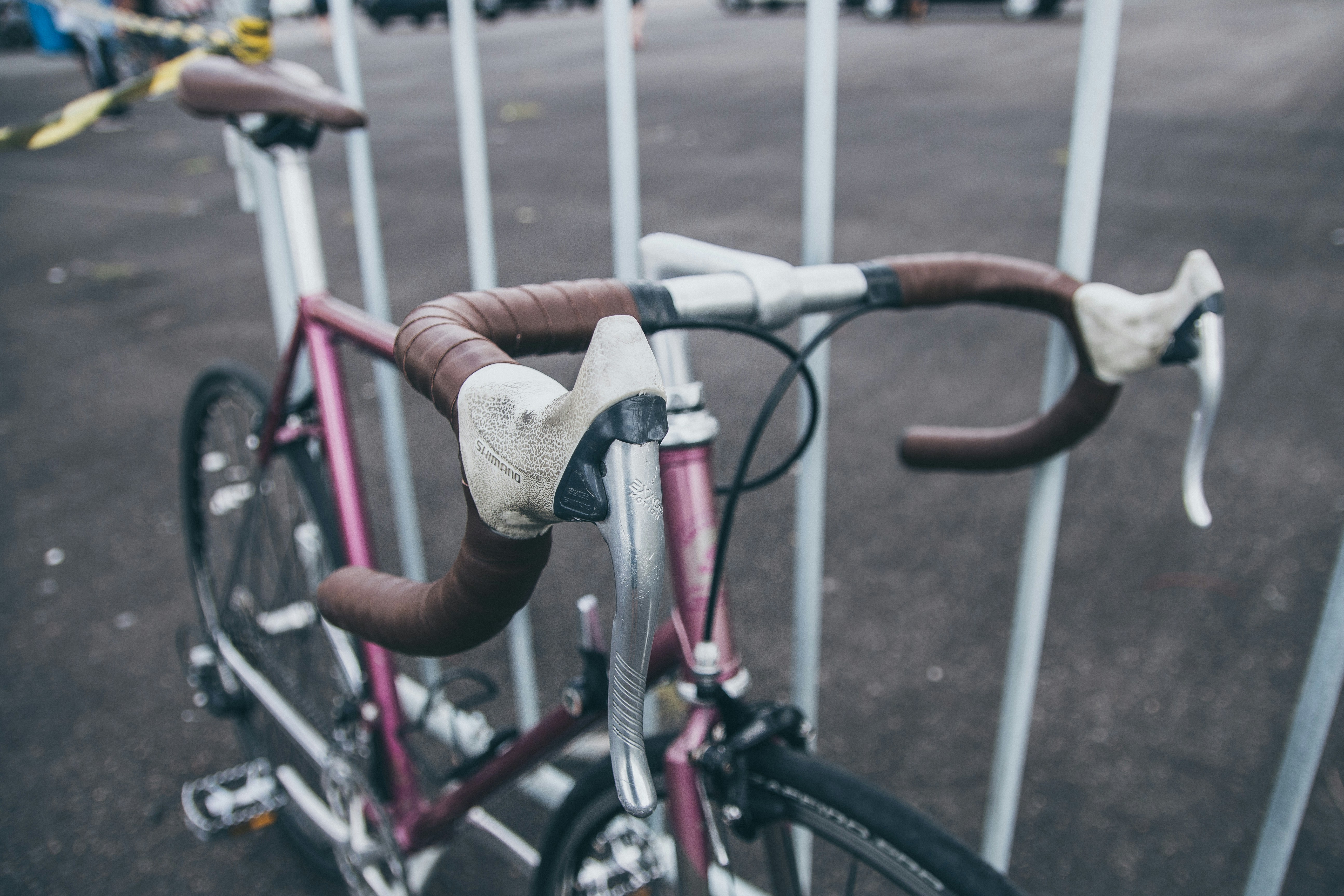 Brown and pink fixed-gear bike leaning against a metal fence on an asphalt surface.