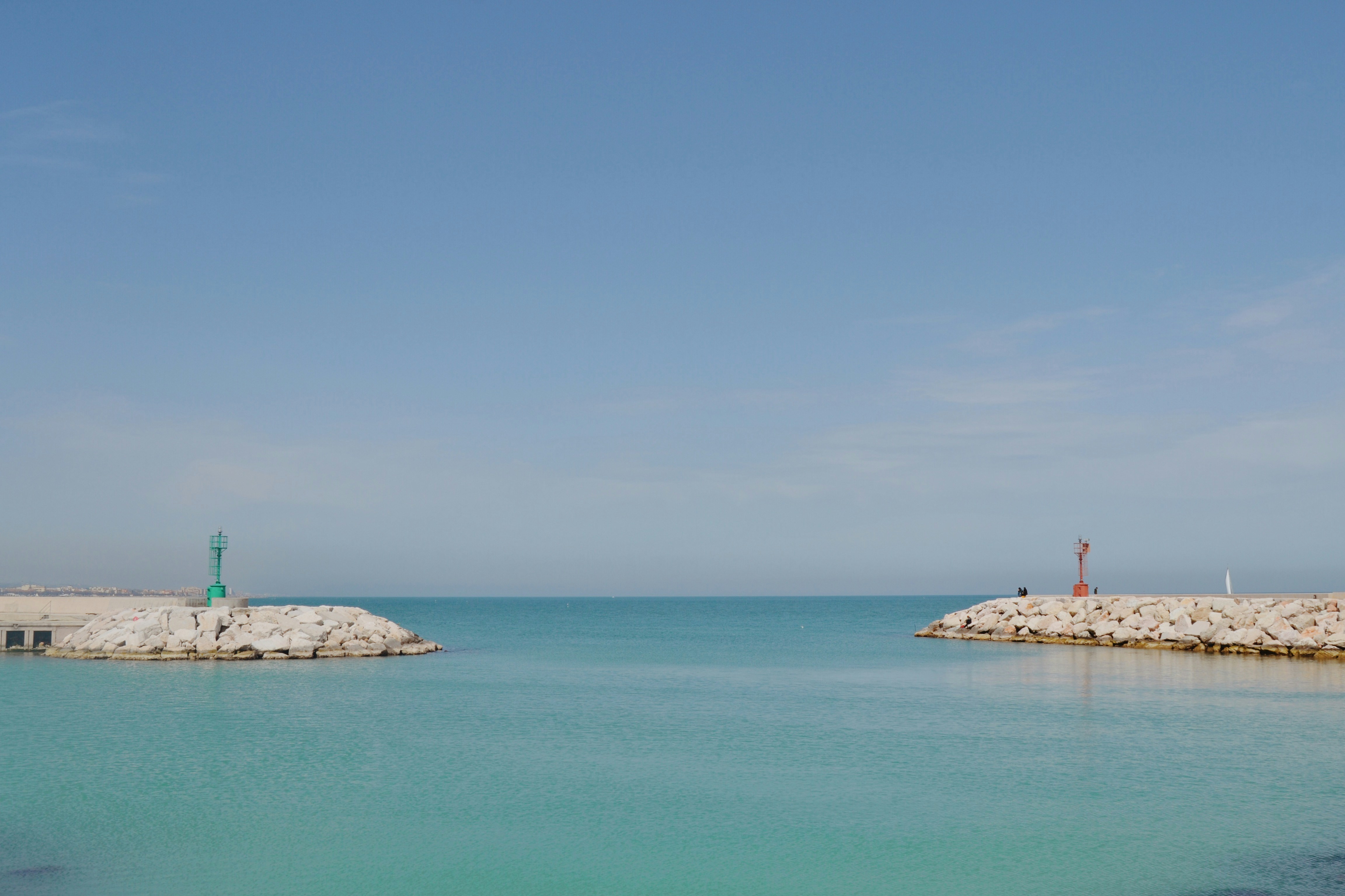 Calm turquoise sea framed by two stone jetties under a clear blue sky.