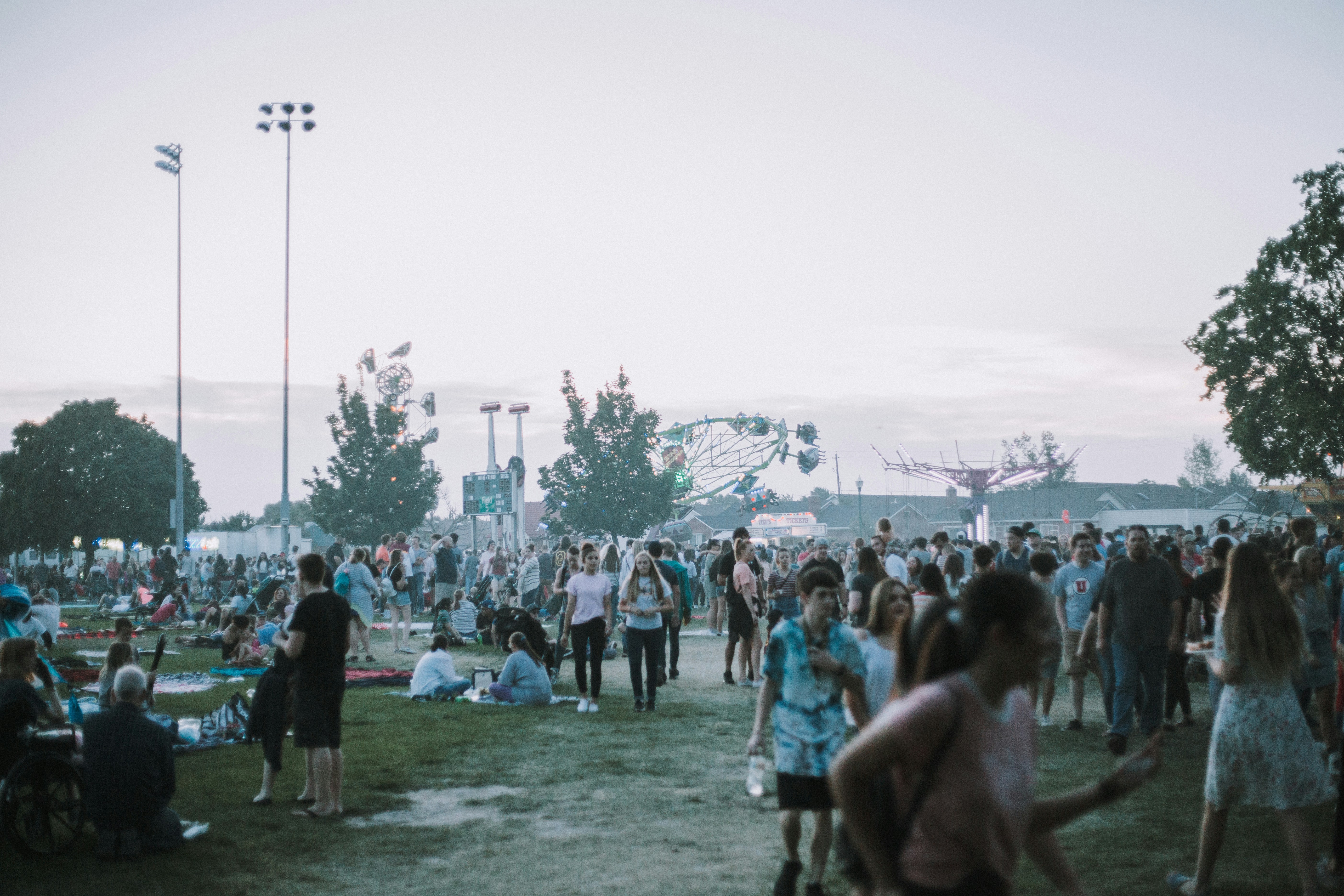 Crowds enjoying an outdoor festival with rides and activities at dusk.