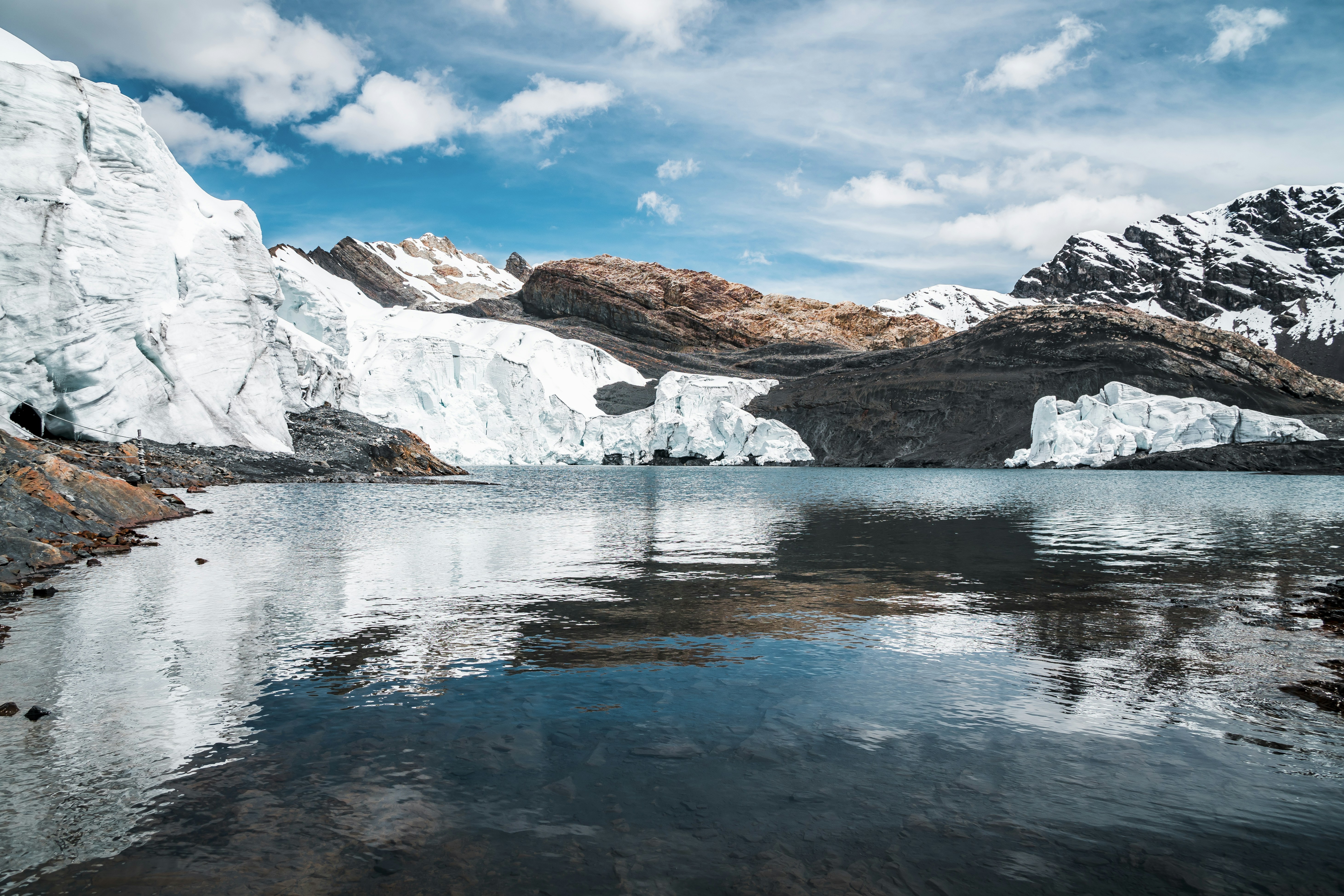 Majestic glacier and rugged mountains reflected in a tranquil lake under a bright blue sky.