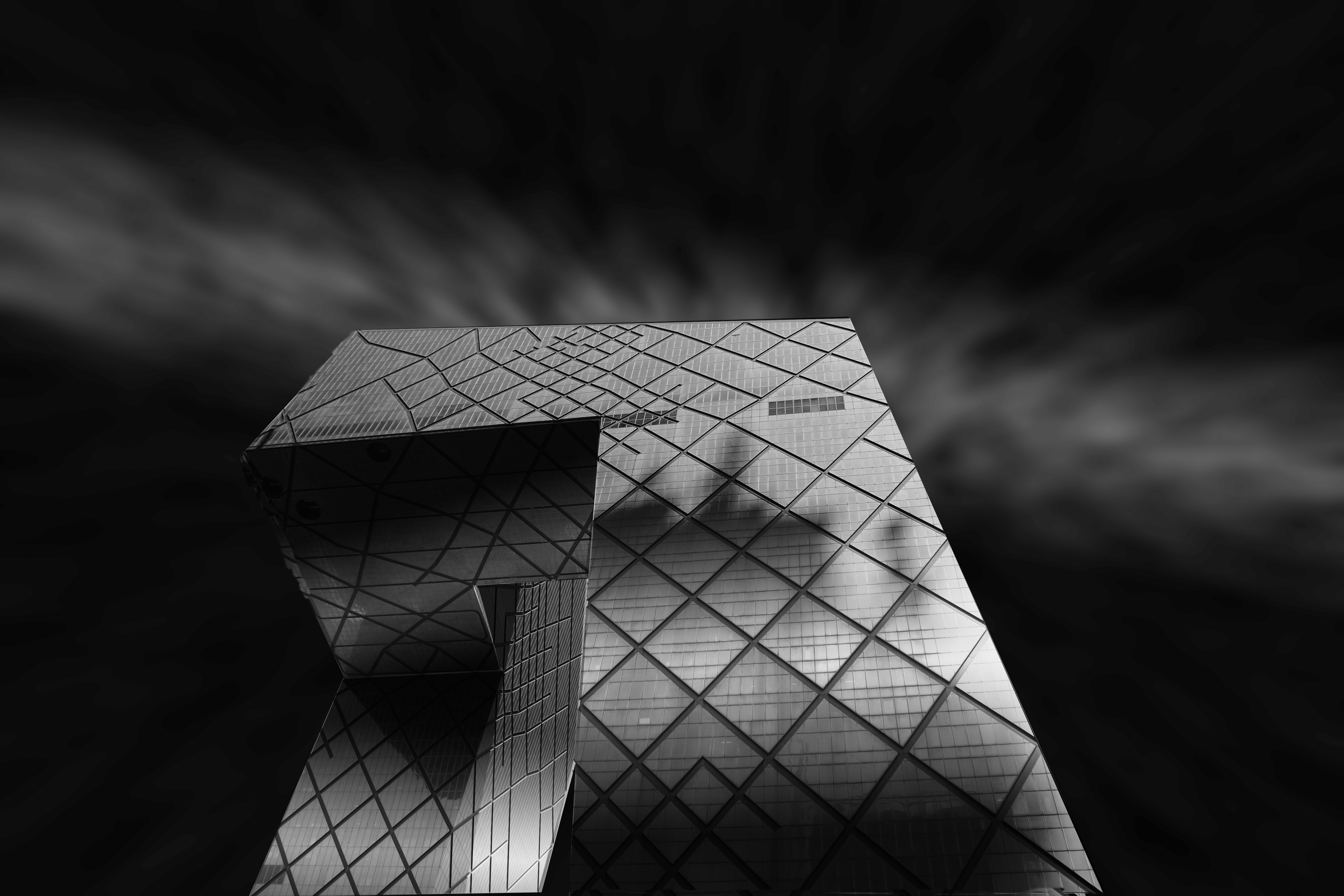 Monochrome view of the CCTV Headquarters, highlighting its geometric design and towering presence against a dramatic sky.