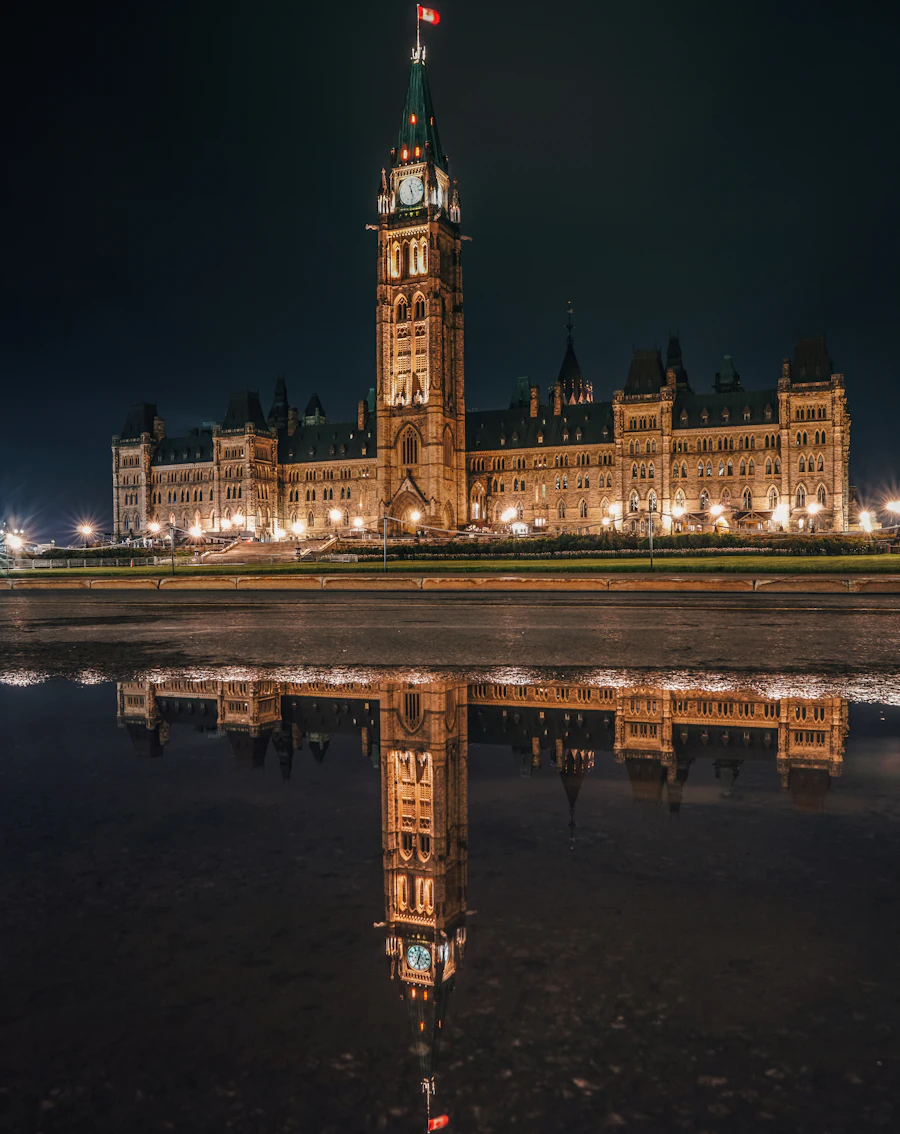 Parliament Hill illuminated at night, featuring the iconic clock tower and its reflection in the water below.