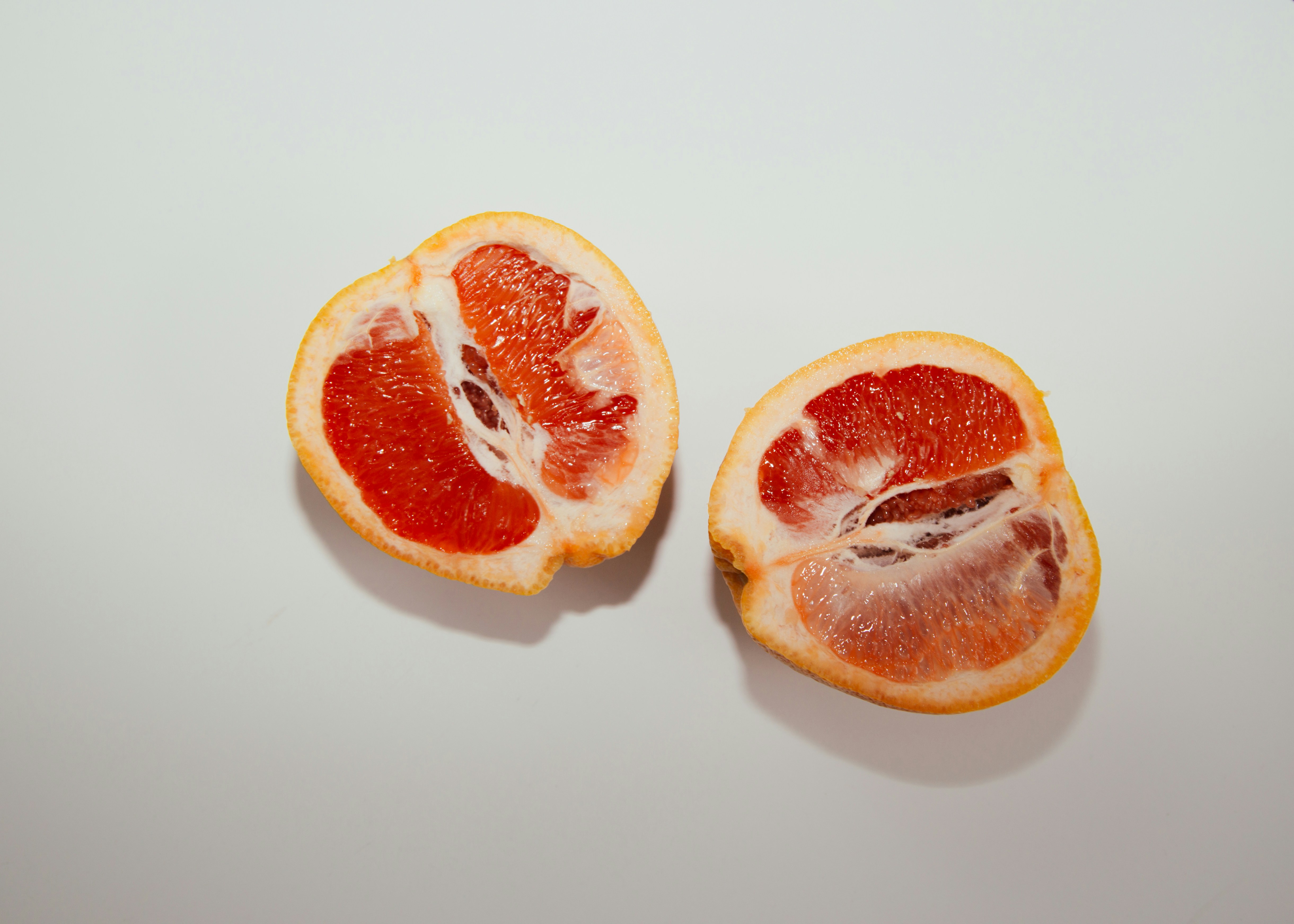 Freshly sliced grapefruit halves revealing vibrant red and pink segments against a clean, minimal background.