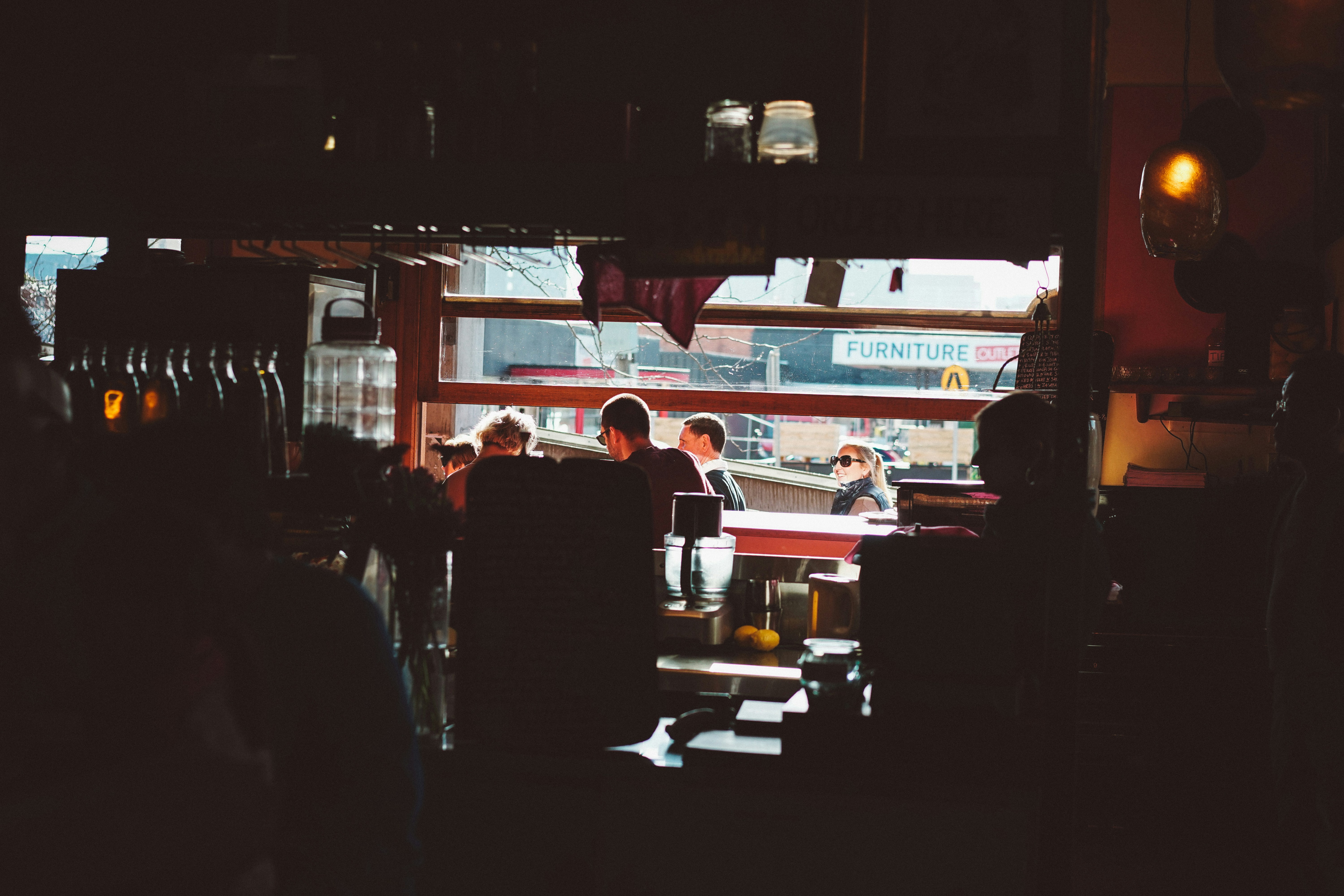 People gathered around a sunlit cafe window, silhouetted against a bustling street scene.