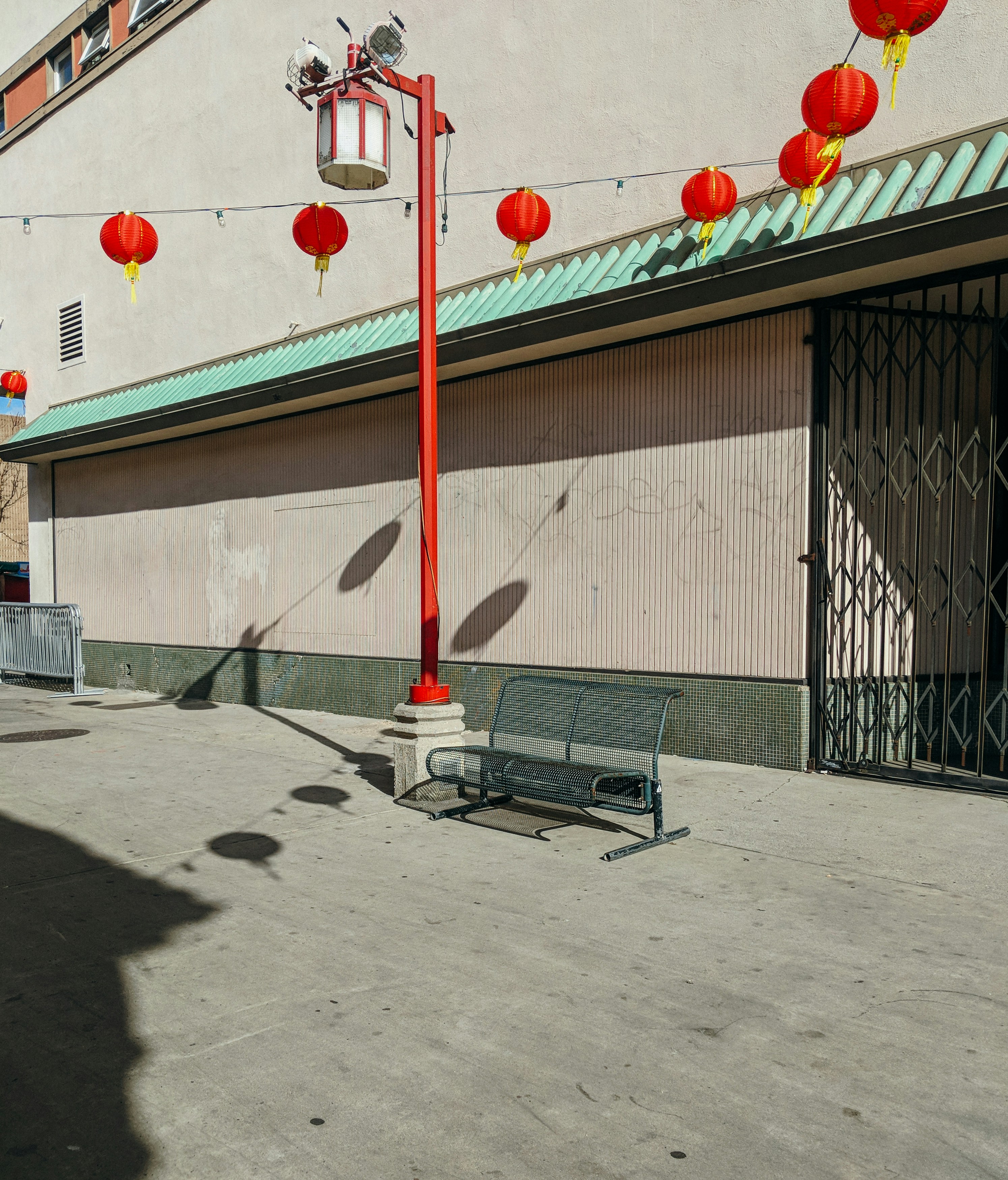 Vibrant red lanterns suspended above a quiet urban street, highlighting a decorative pole and an empty bench. 