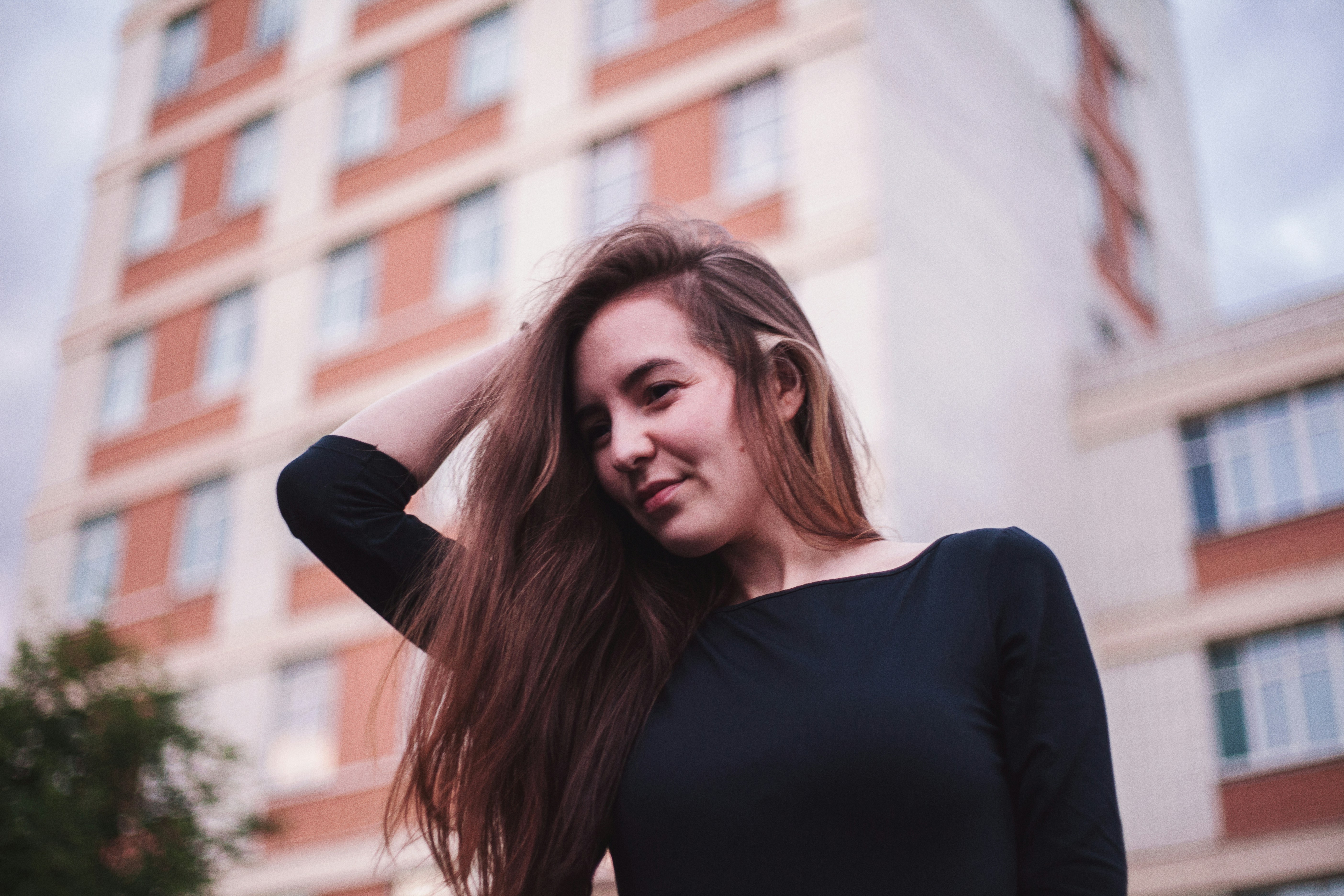 Young woman with long hair playfully posing against a modern building backdrop during twilight.