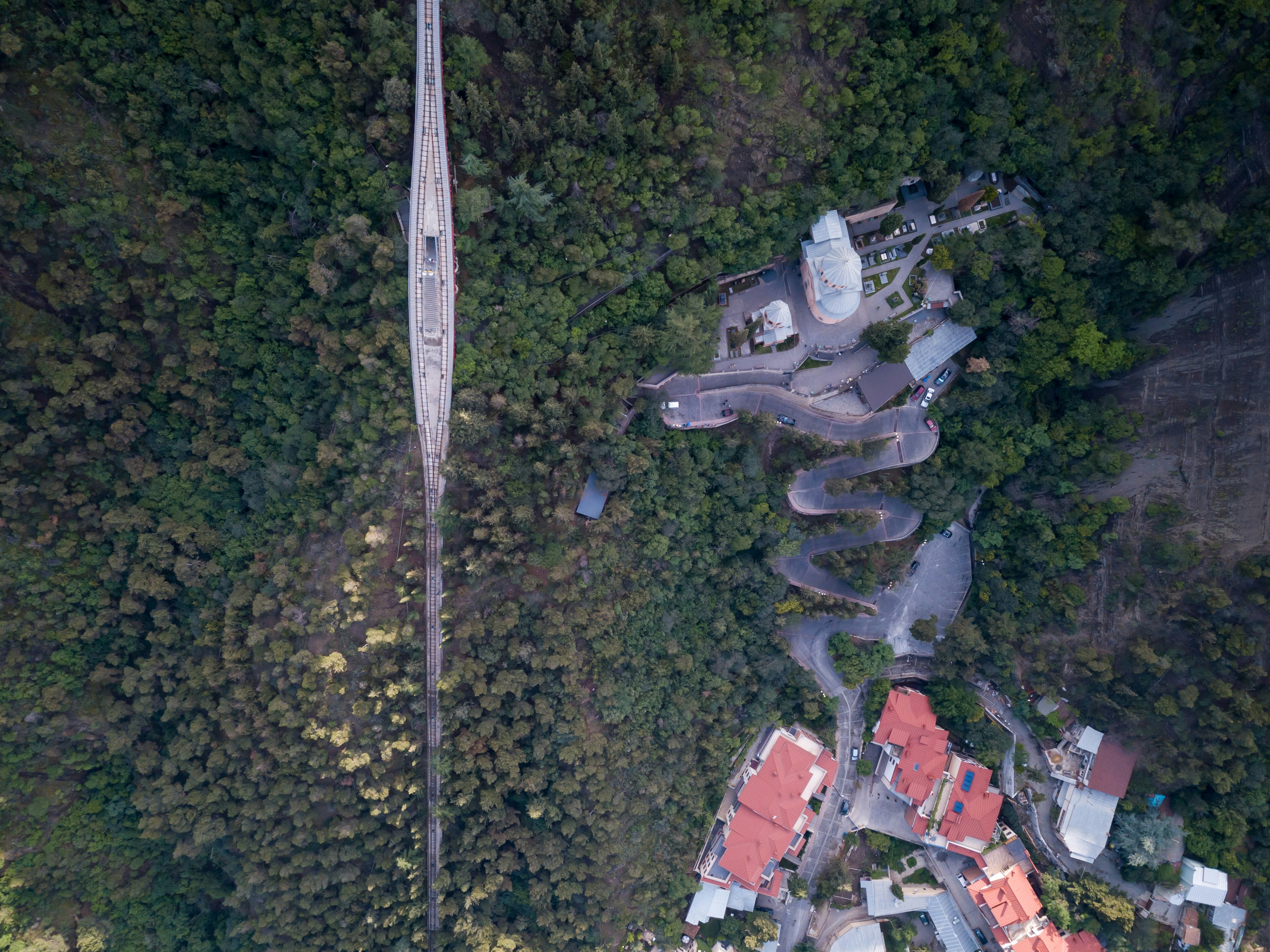 Aerial view of a funicular railway cutting through lush greenery alongside winding roads and buildings.