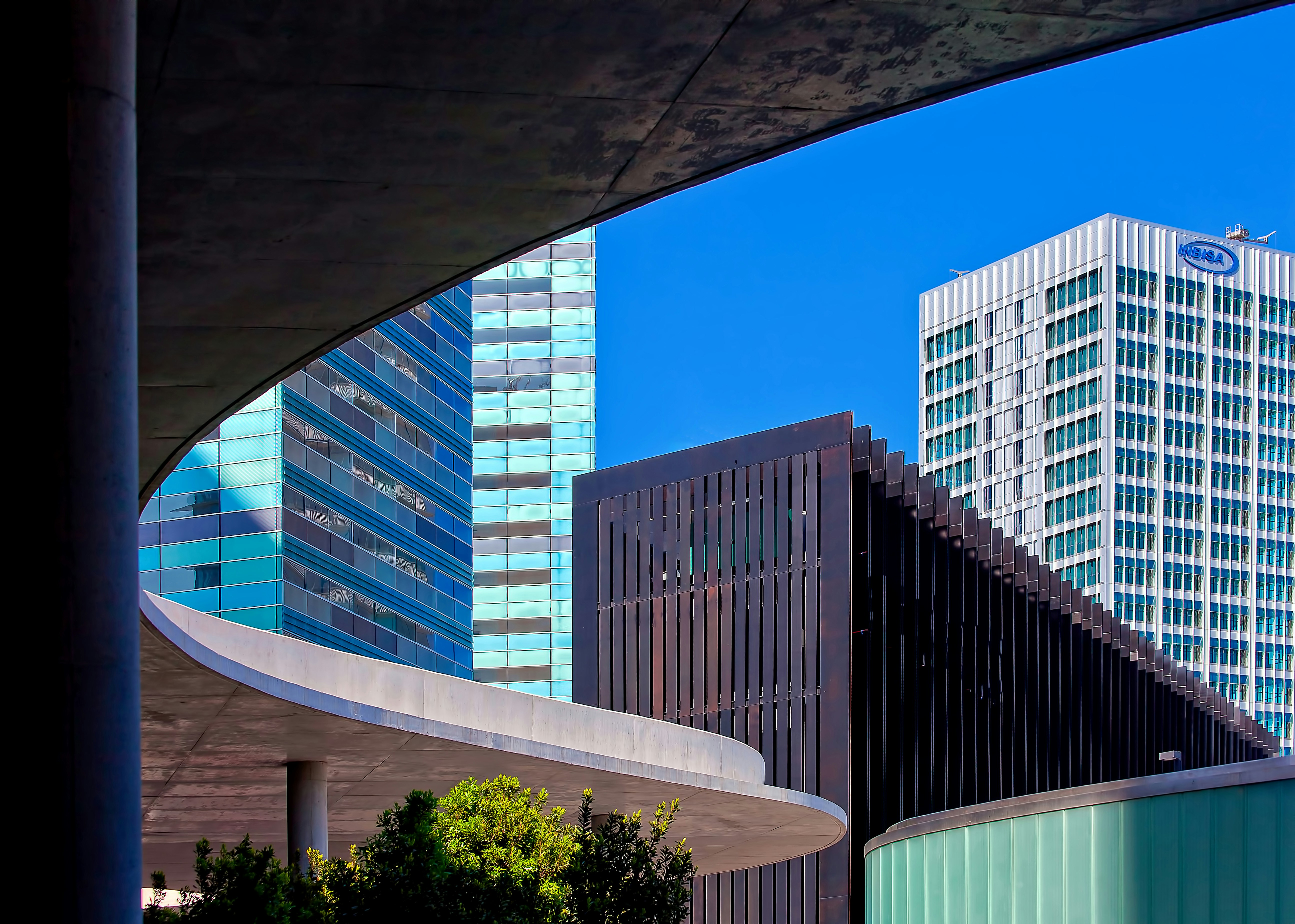 Modern architecture featuring sleek glass buildings and curved concrete structures under a clear blue sky.