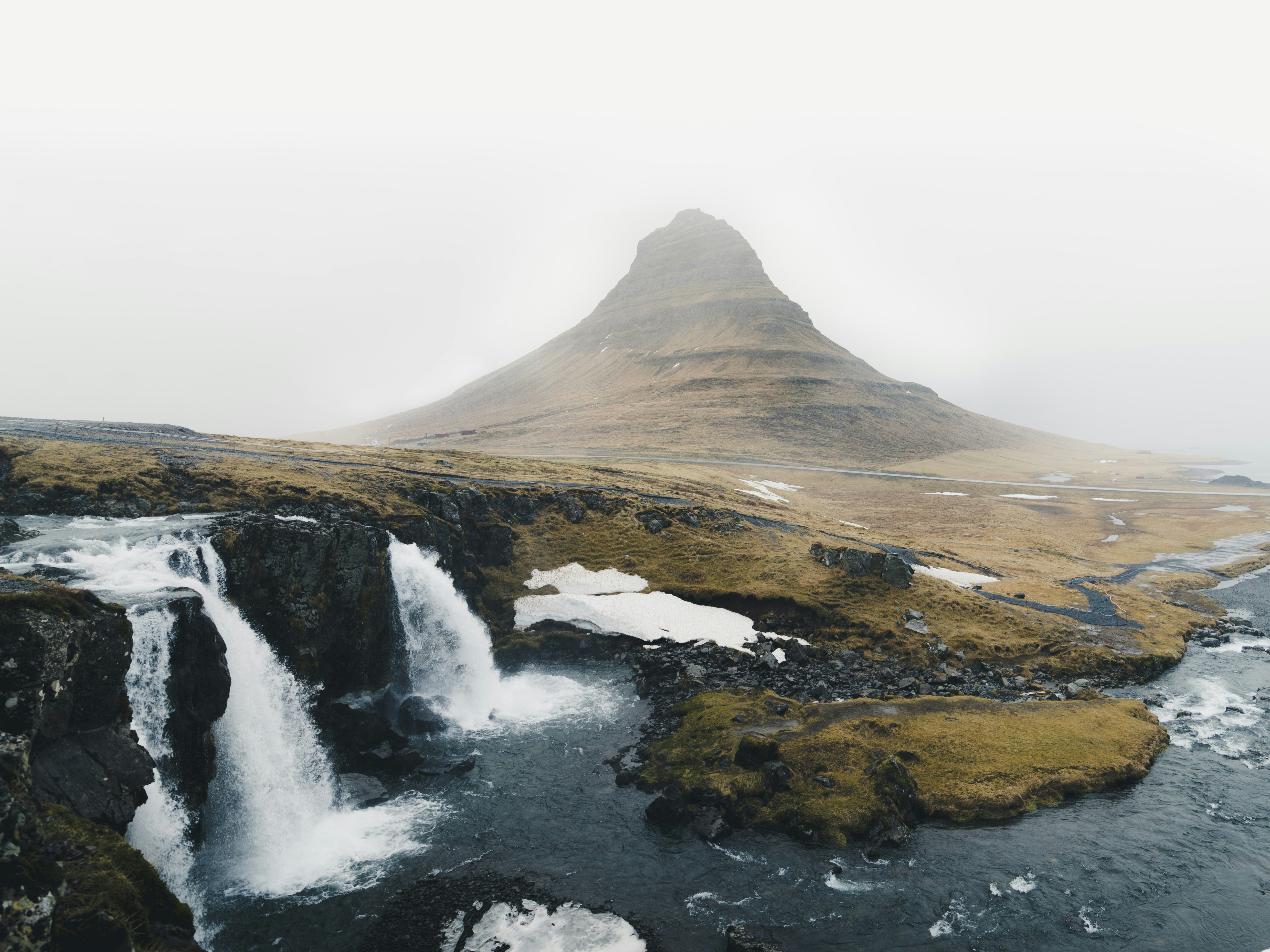 Majestic waterfall cascading into a river with Kirkjufell mountain shrouded in mist in the background.