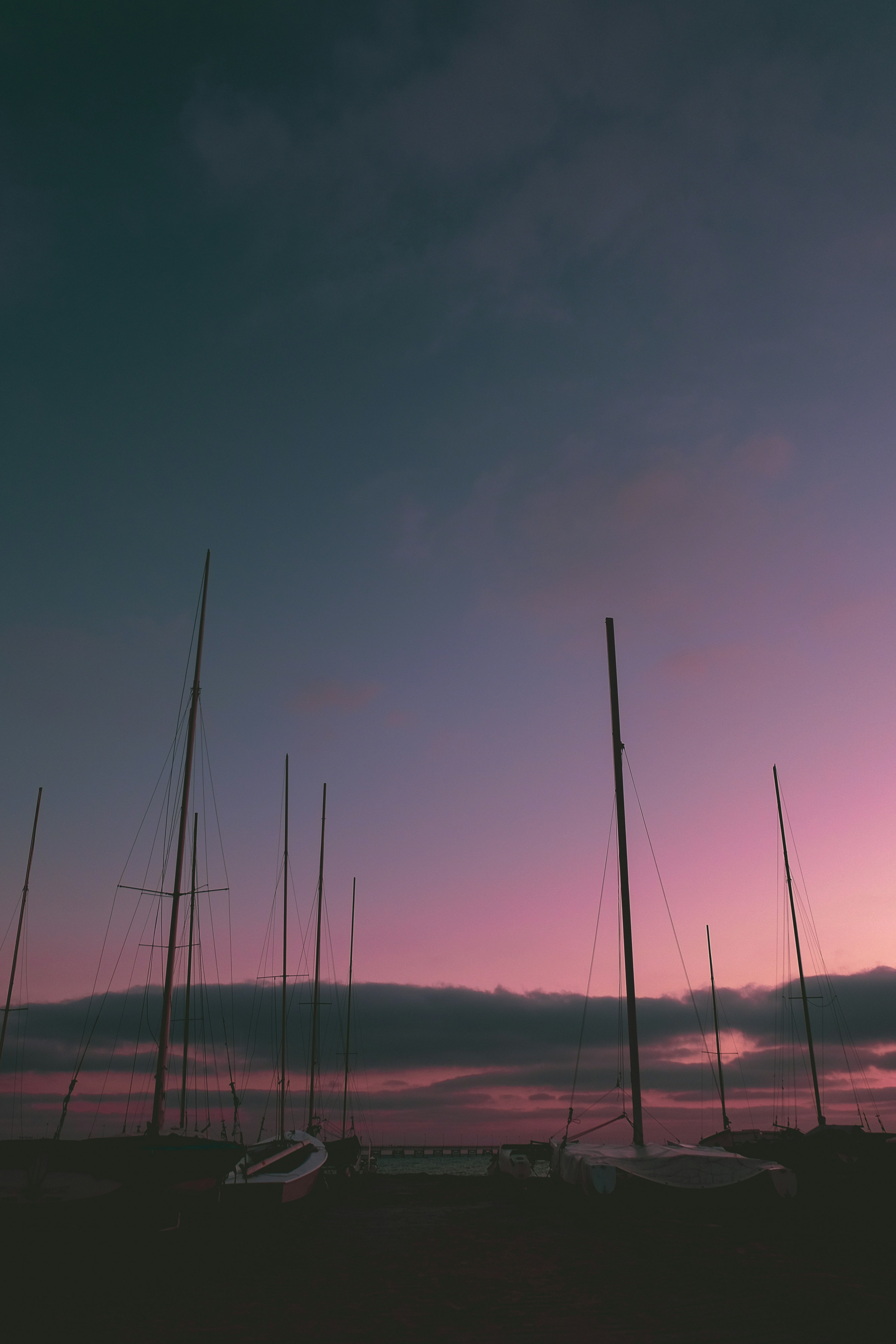 Silhouettes of sailboats and masts set against a gradient twilight sky, transitioning from deep blue to soft pink hues.