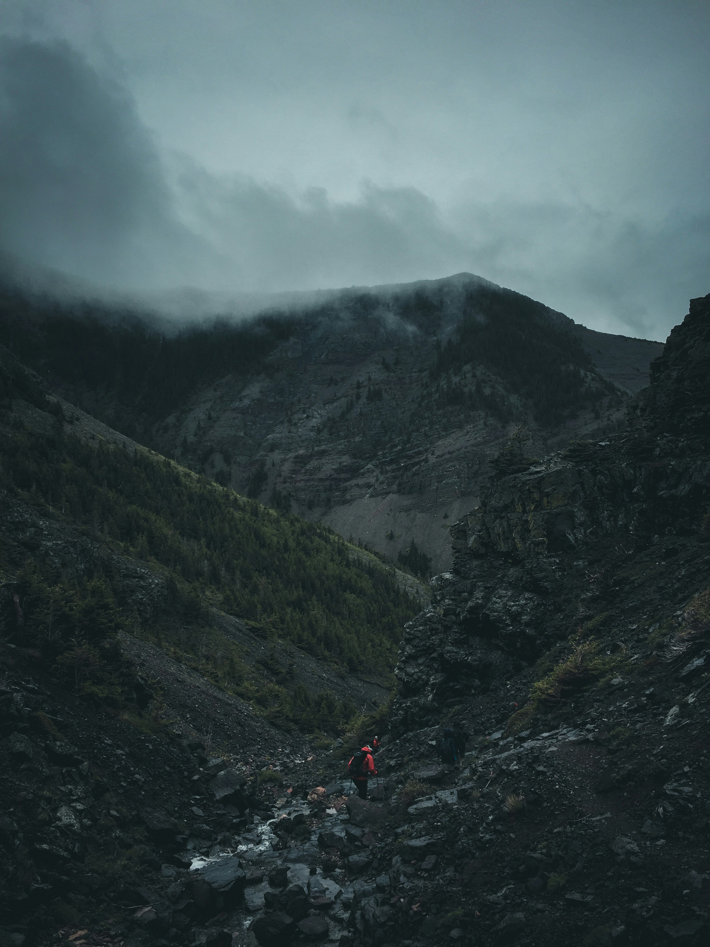 Red-clad climber threads a shadowed gorge beneath a brooding ridge
