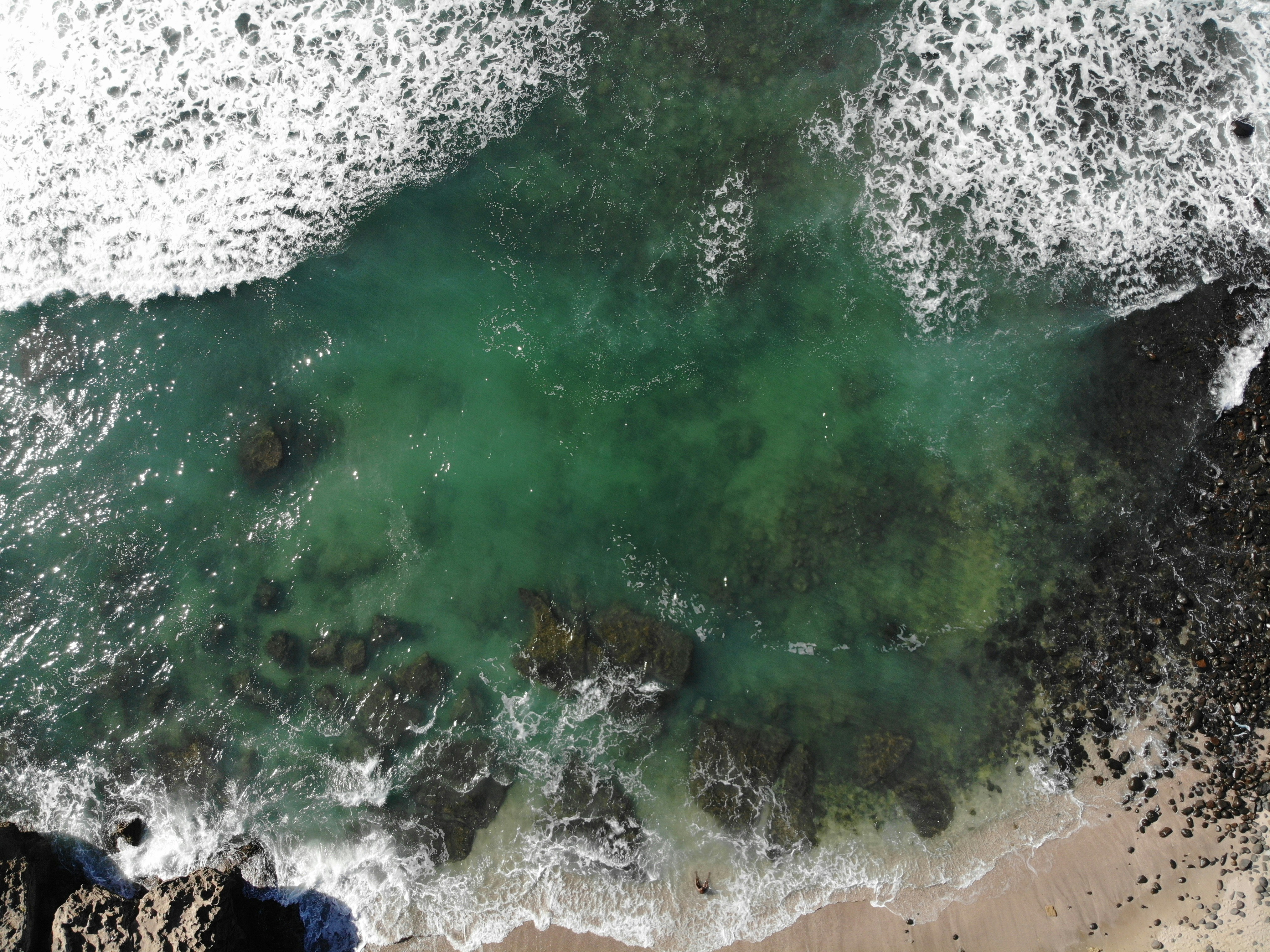 Aerial view of turquoise ocean waves gently meeting a rocky South African beach.