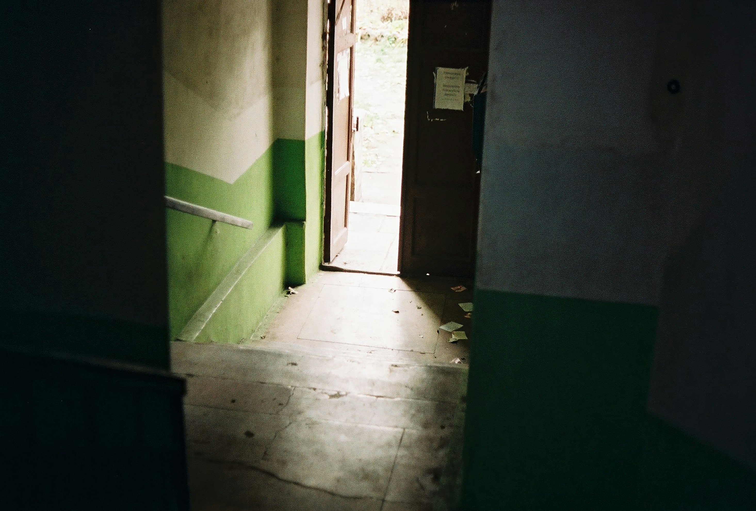 Open door revealing a glimpse of the outdoors, framed by green and beige walls in a dimly lit corridor.