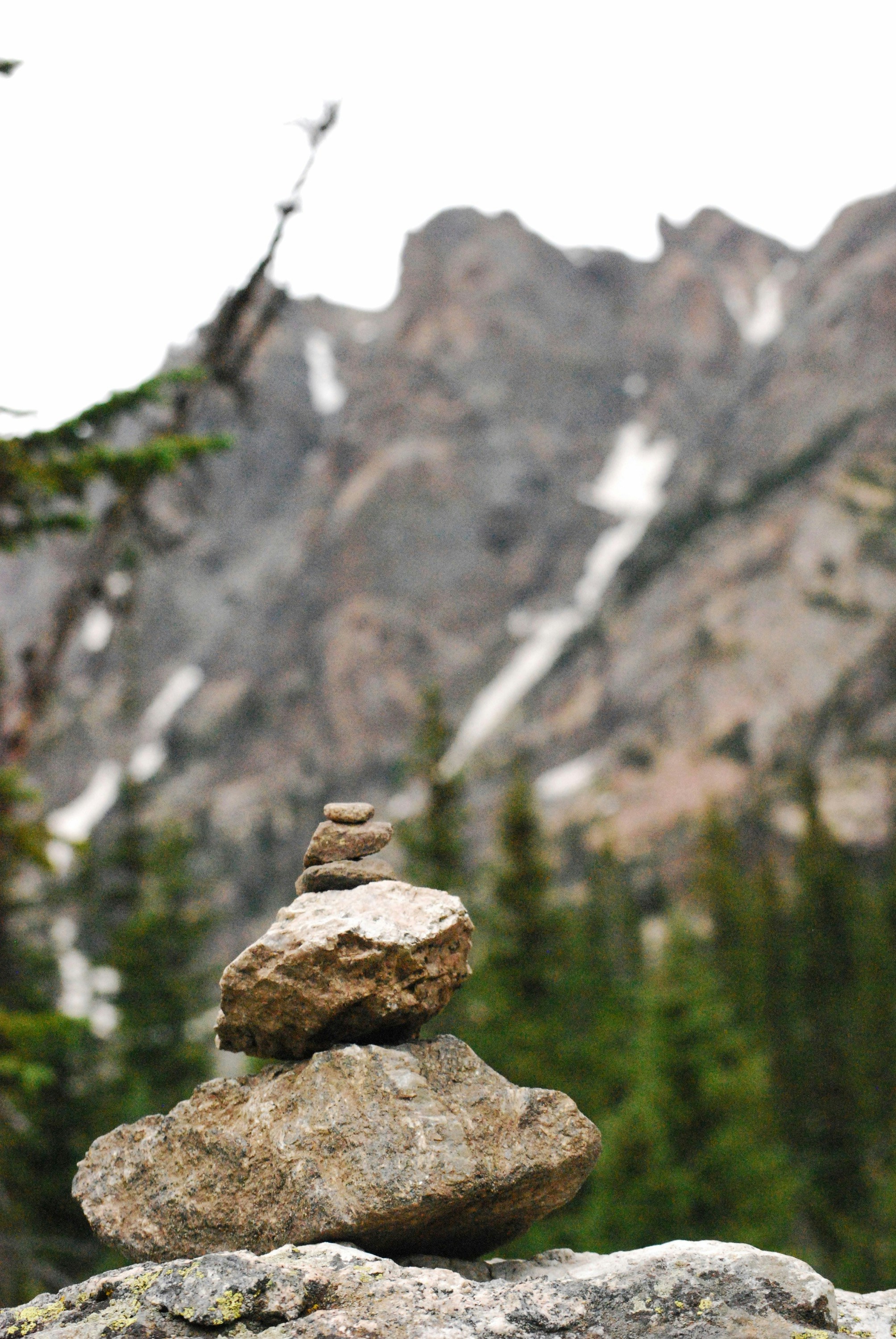 Stacked stones stand resilient against a backdrop of rugged mountains and dense forest, symbolizing harmony with nature.