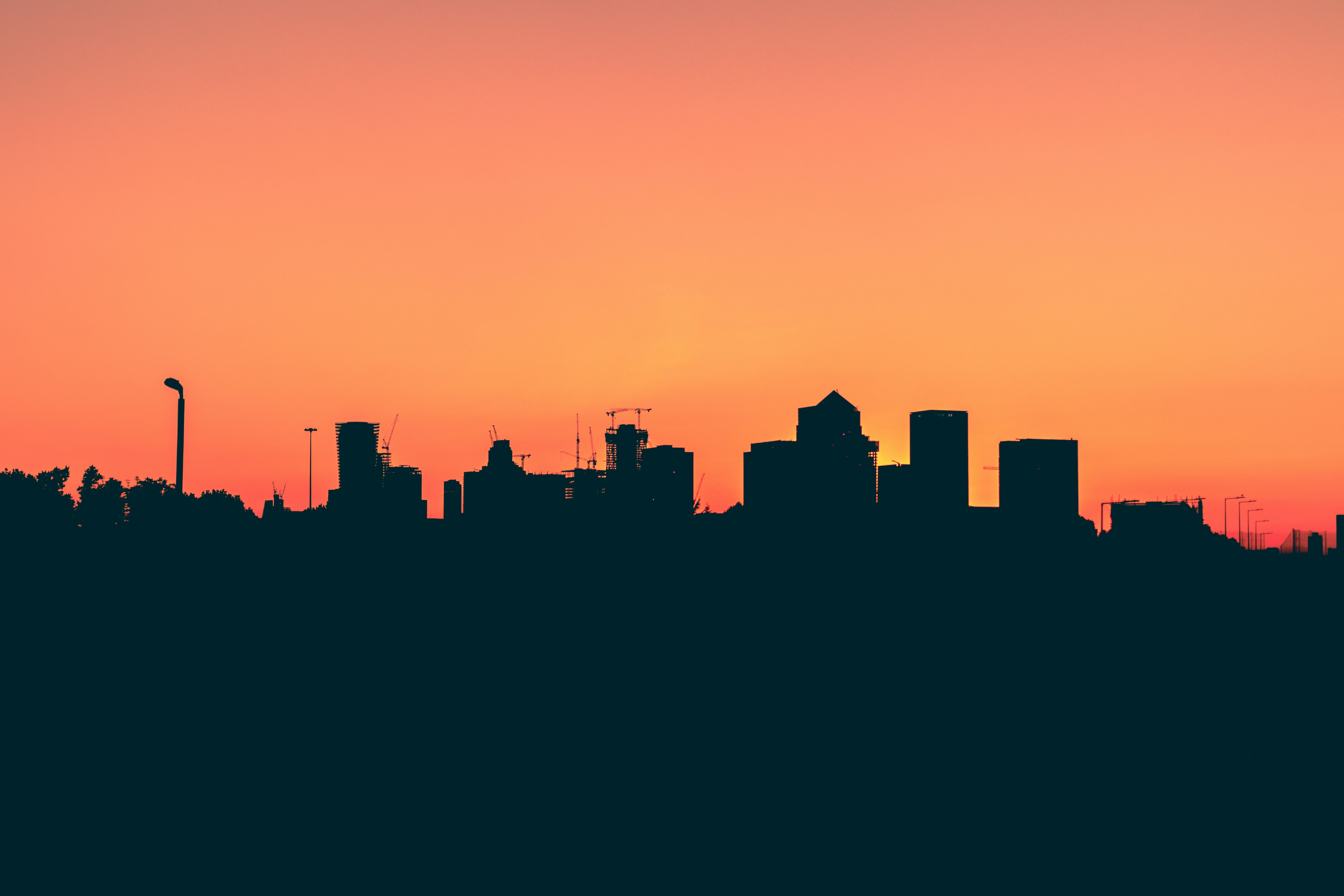 Silhouette of a city skyline beneath a vibrant orange sunset sky.