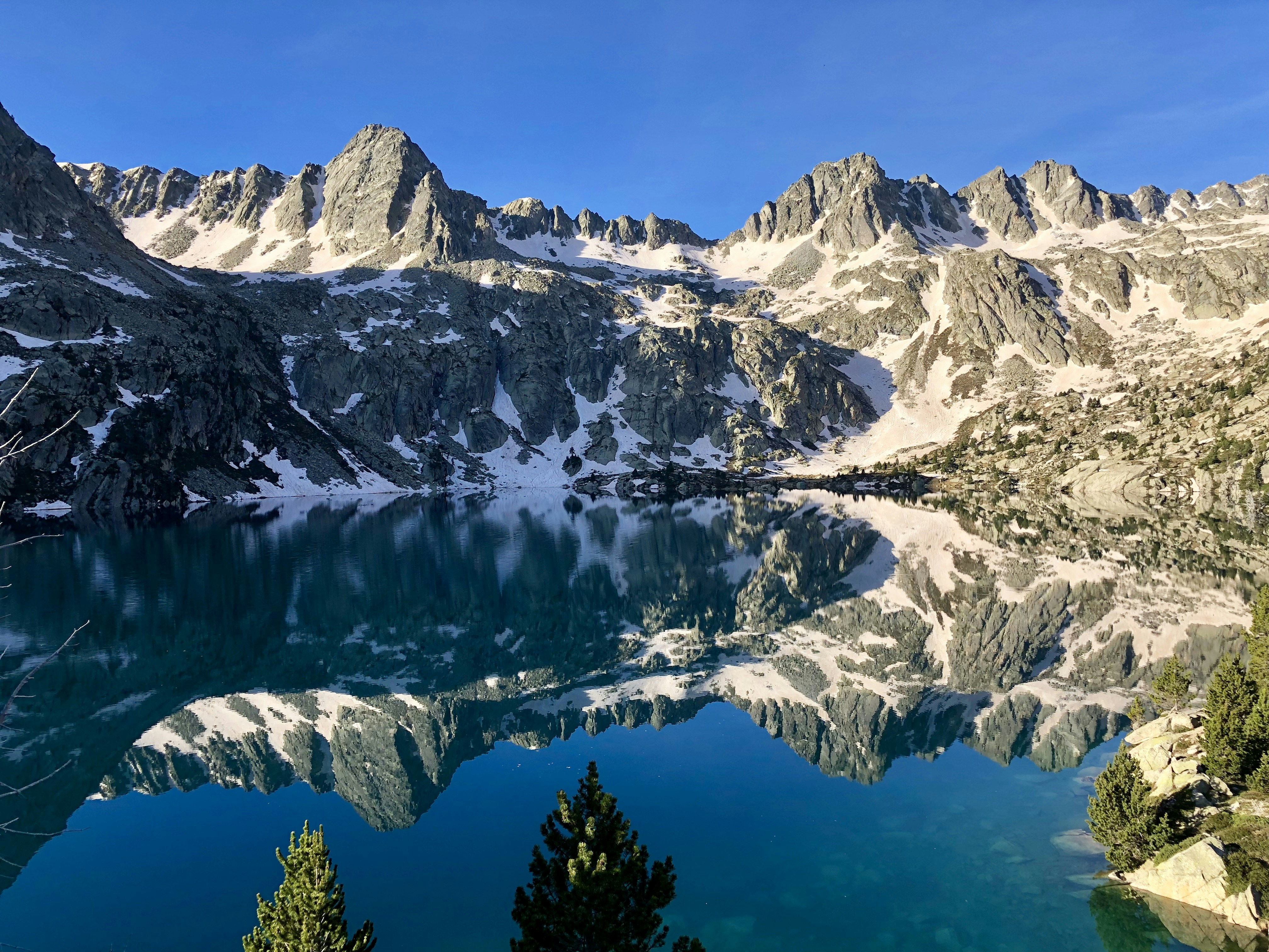 Snow-dusted mountains mirrored perfectly on a tranquil alpine lake under a clear blue sky.