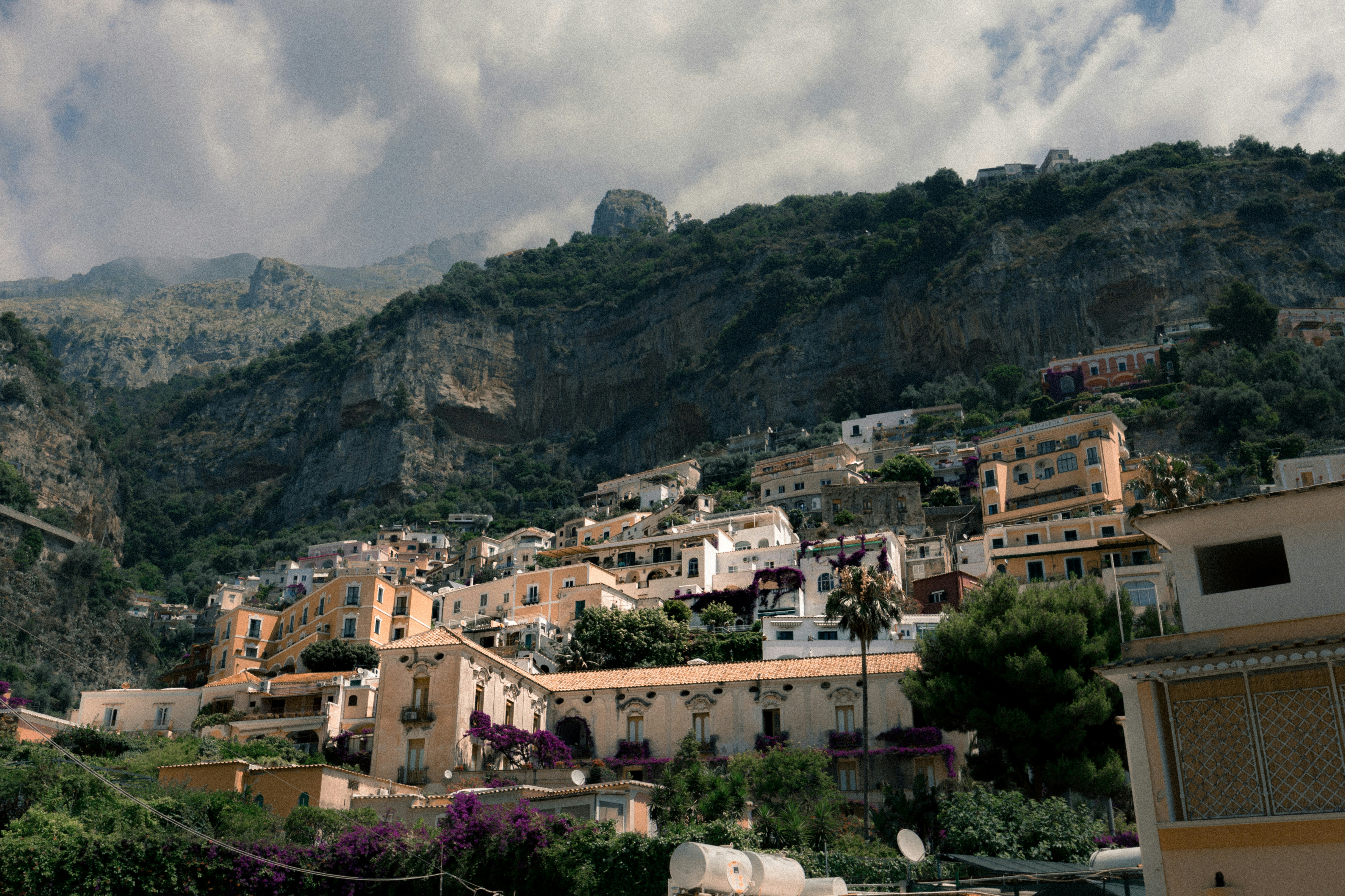 Colorful buildings cascade down a steep cliff under a partially cloudy sky.