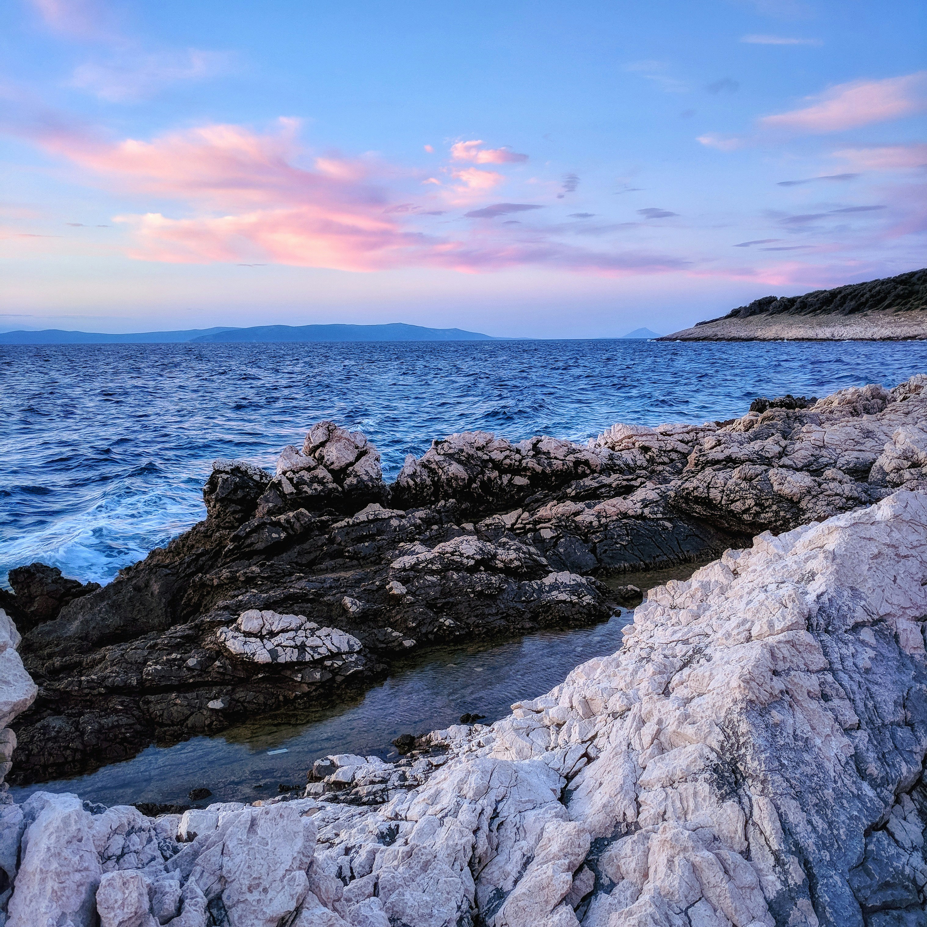 Rocky coastline with waves gently crashing under a pastel sunset sky.