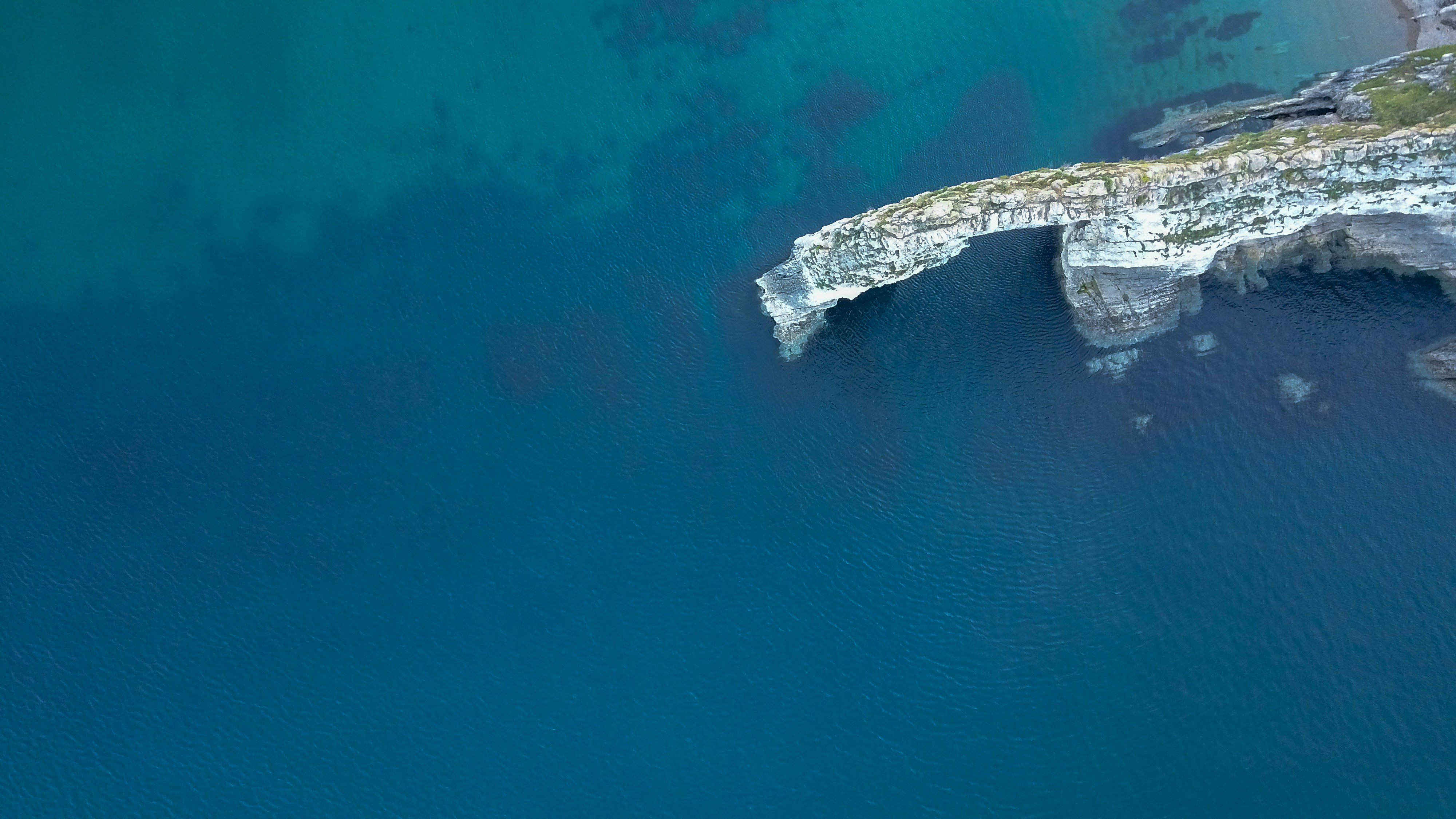 Rocky coastal arch extending over deep blue ocean waters.