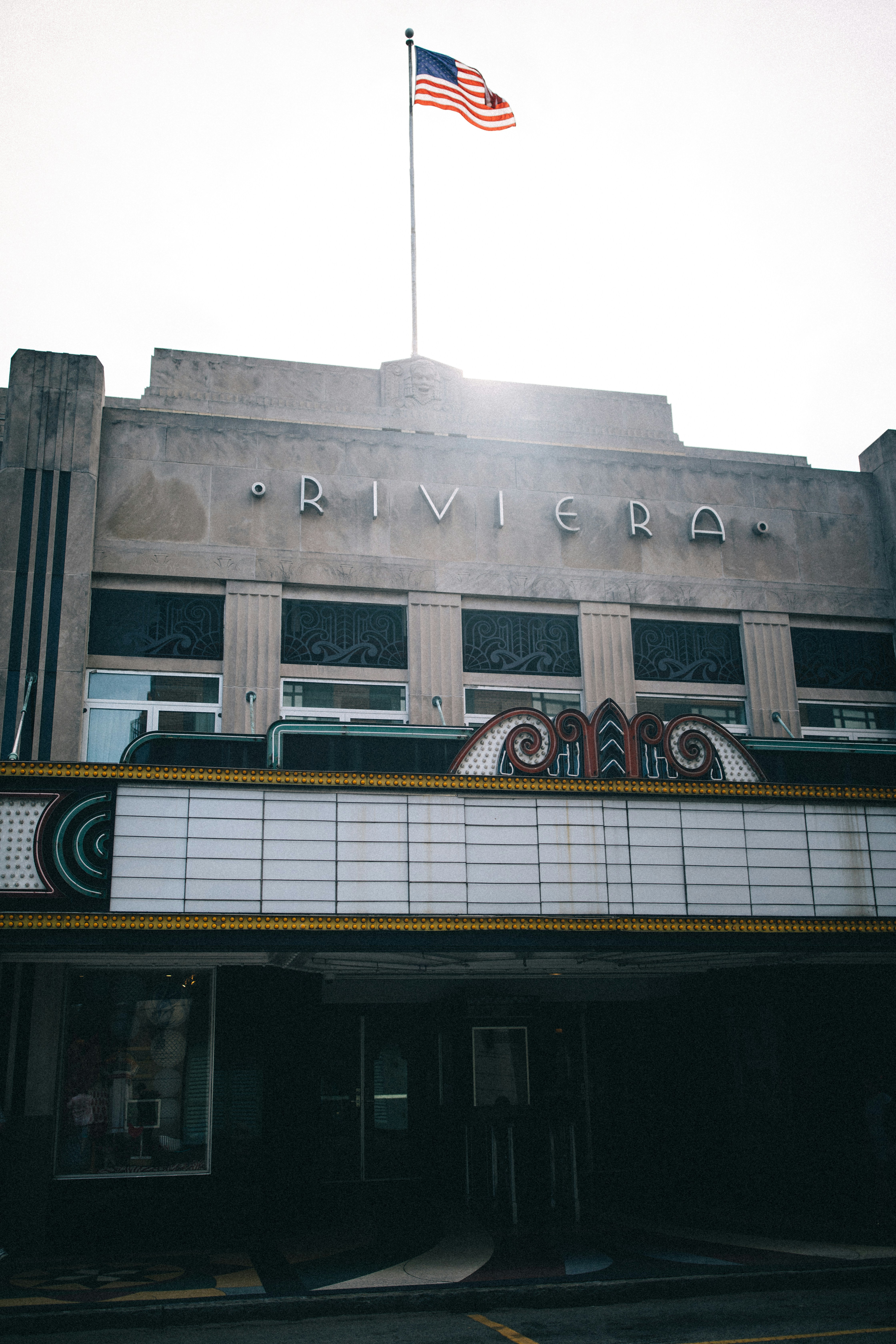 Art Deco theater entrance with a marquee and an American flag waving above.