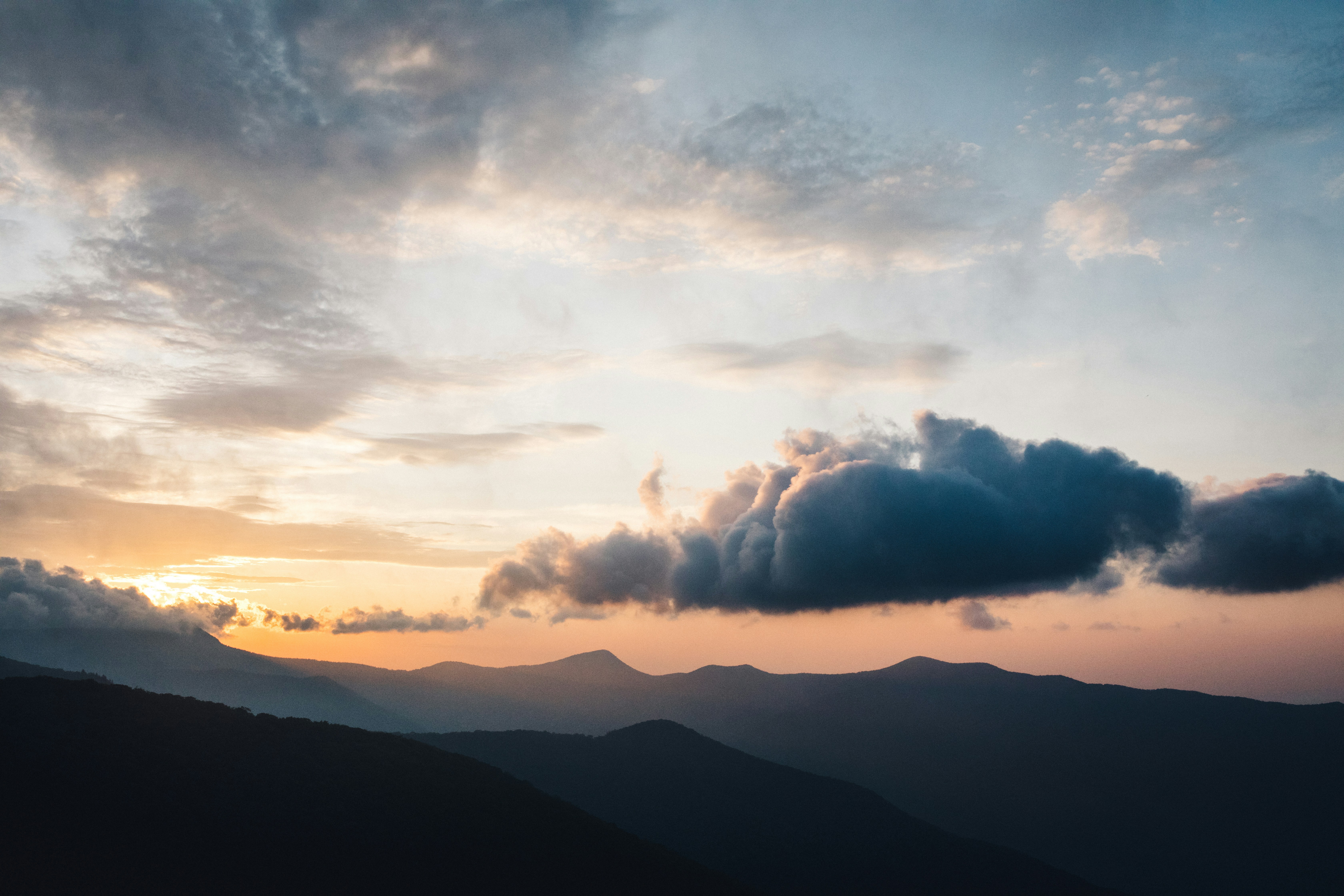 Golden sunset illuminating distant mountains beneath a textured sky with dramatic clouds.