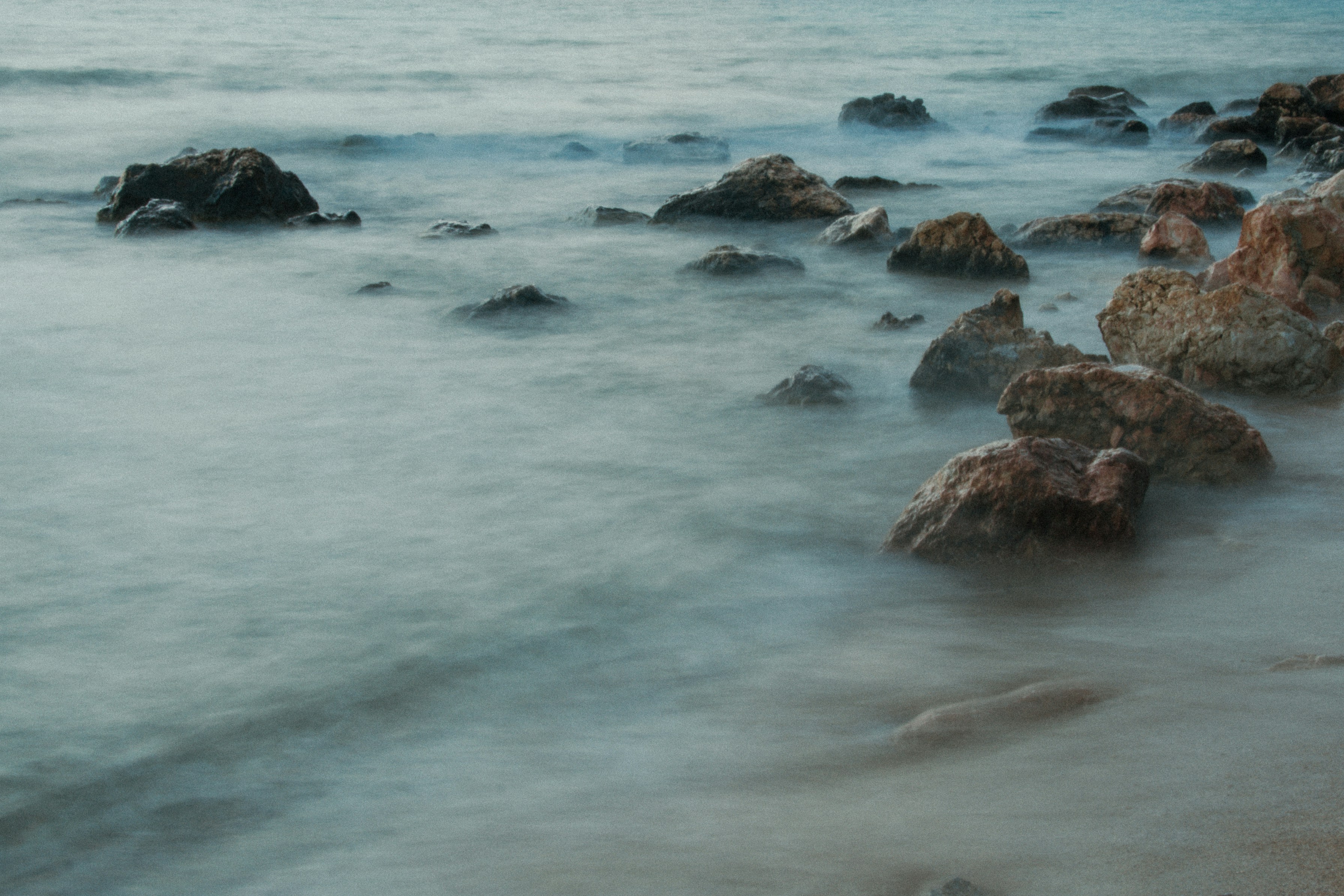 Gentle waves wash over a rocky shoreline under a soft, misty sky.