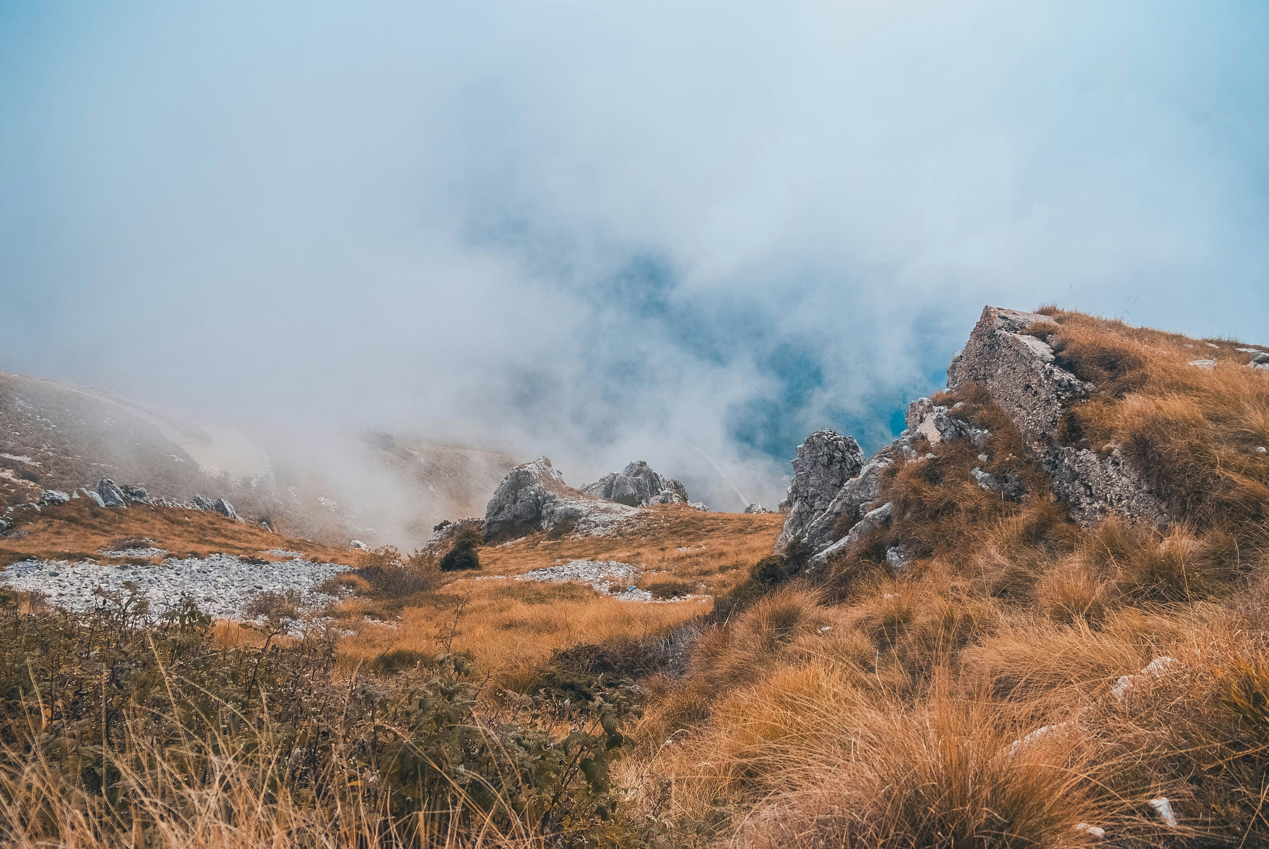 Rolling mist sweeps over rugged rocks and golden grass on a serene mountainside.