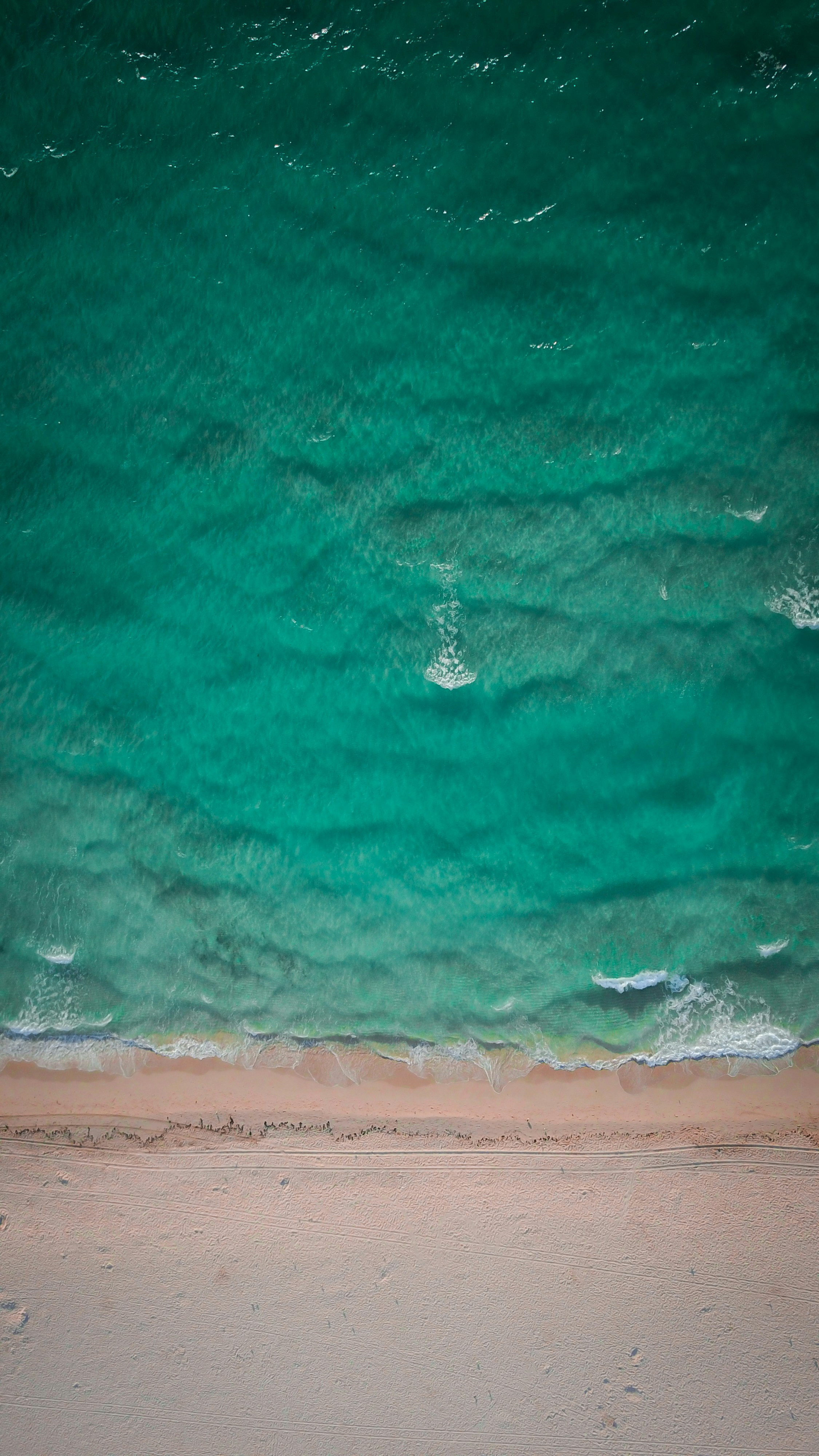 Aerial view of turquoise ocean meeting a sandy beach, showcasing gentle waves lapping at the shore.