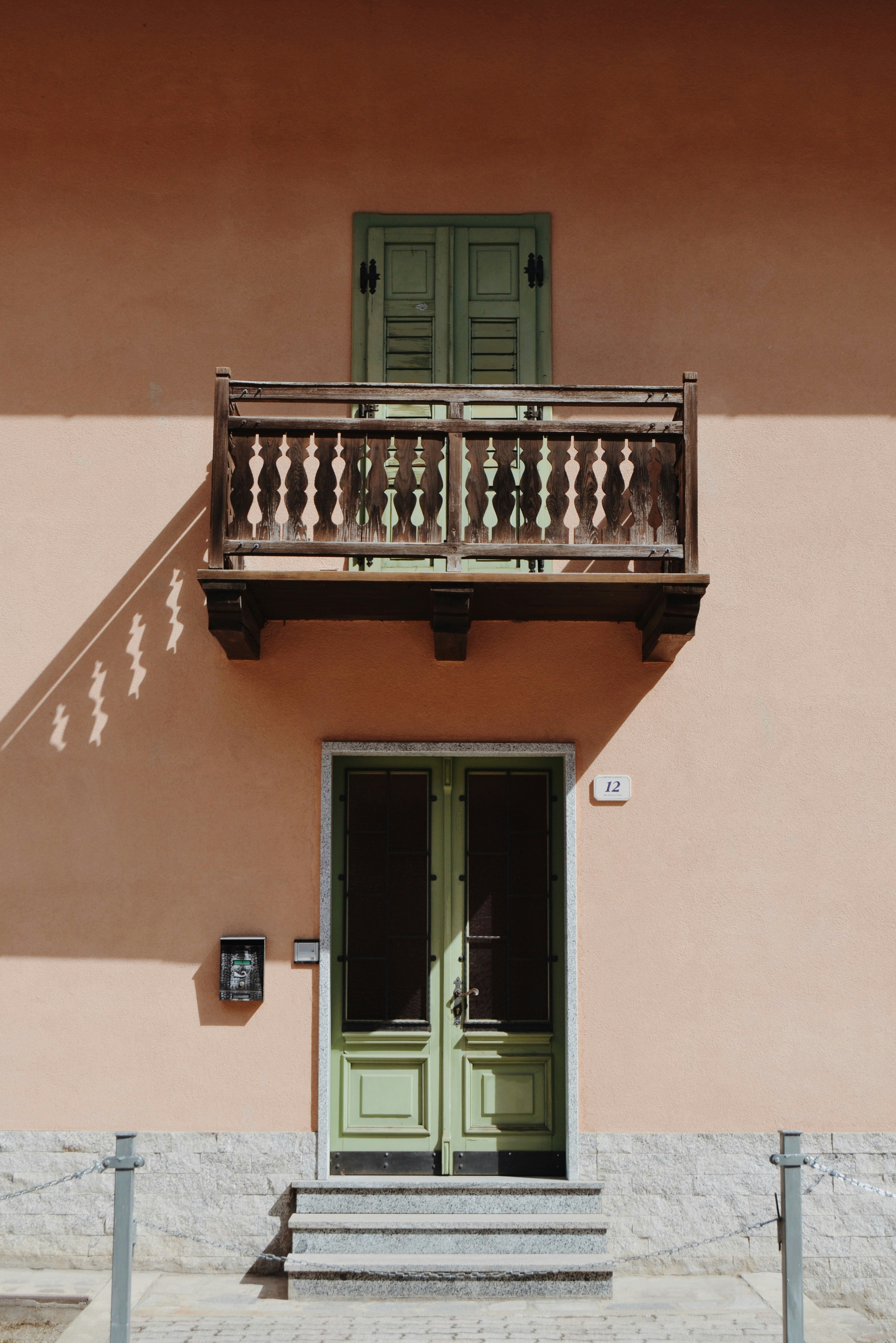 Green double doors framed by a rustic balcony and soft peach walls, showcasing architectural elegance and warmth.