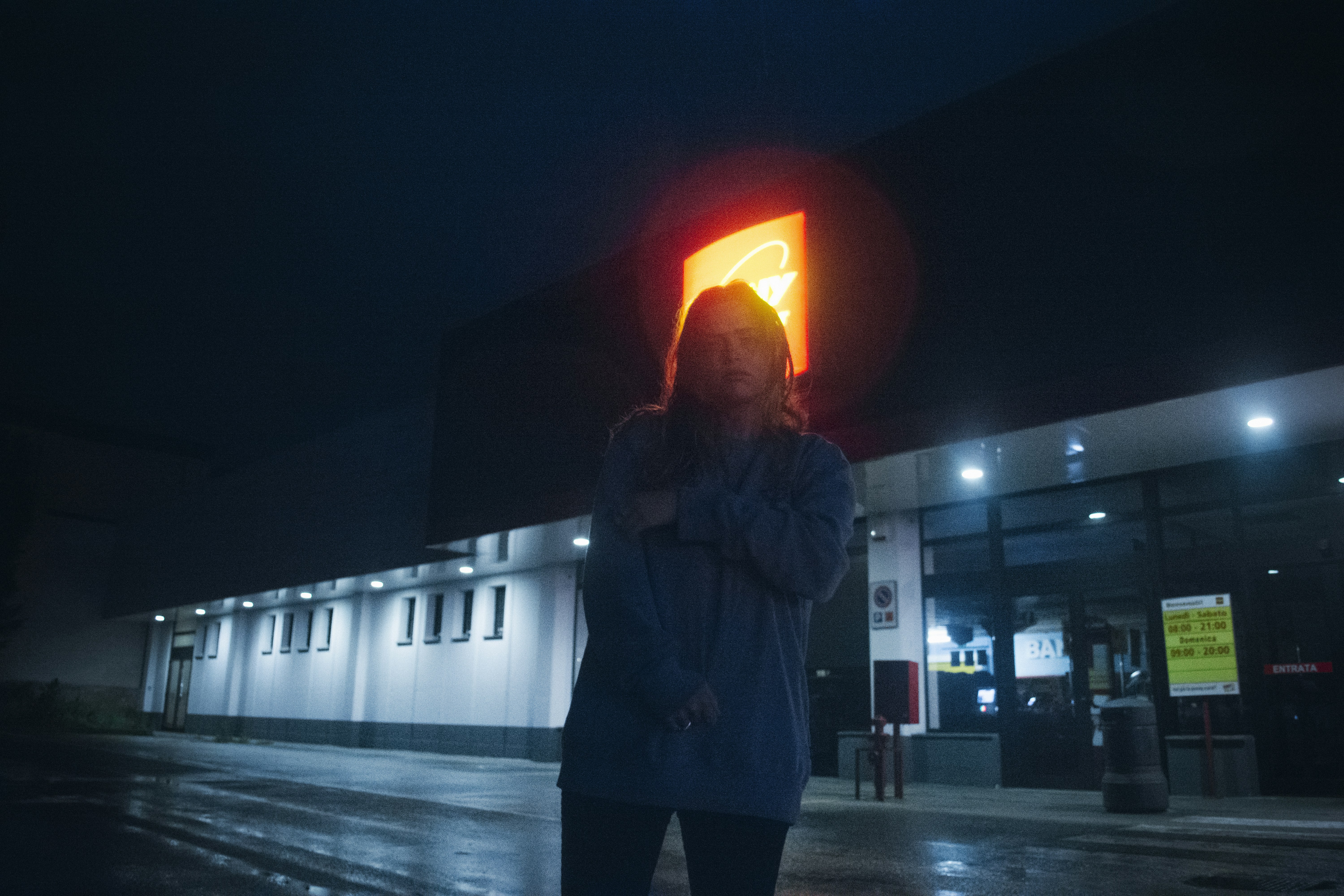 Person standing in front of a building illuminated by neon lights on a rainy night.
