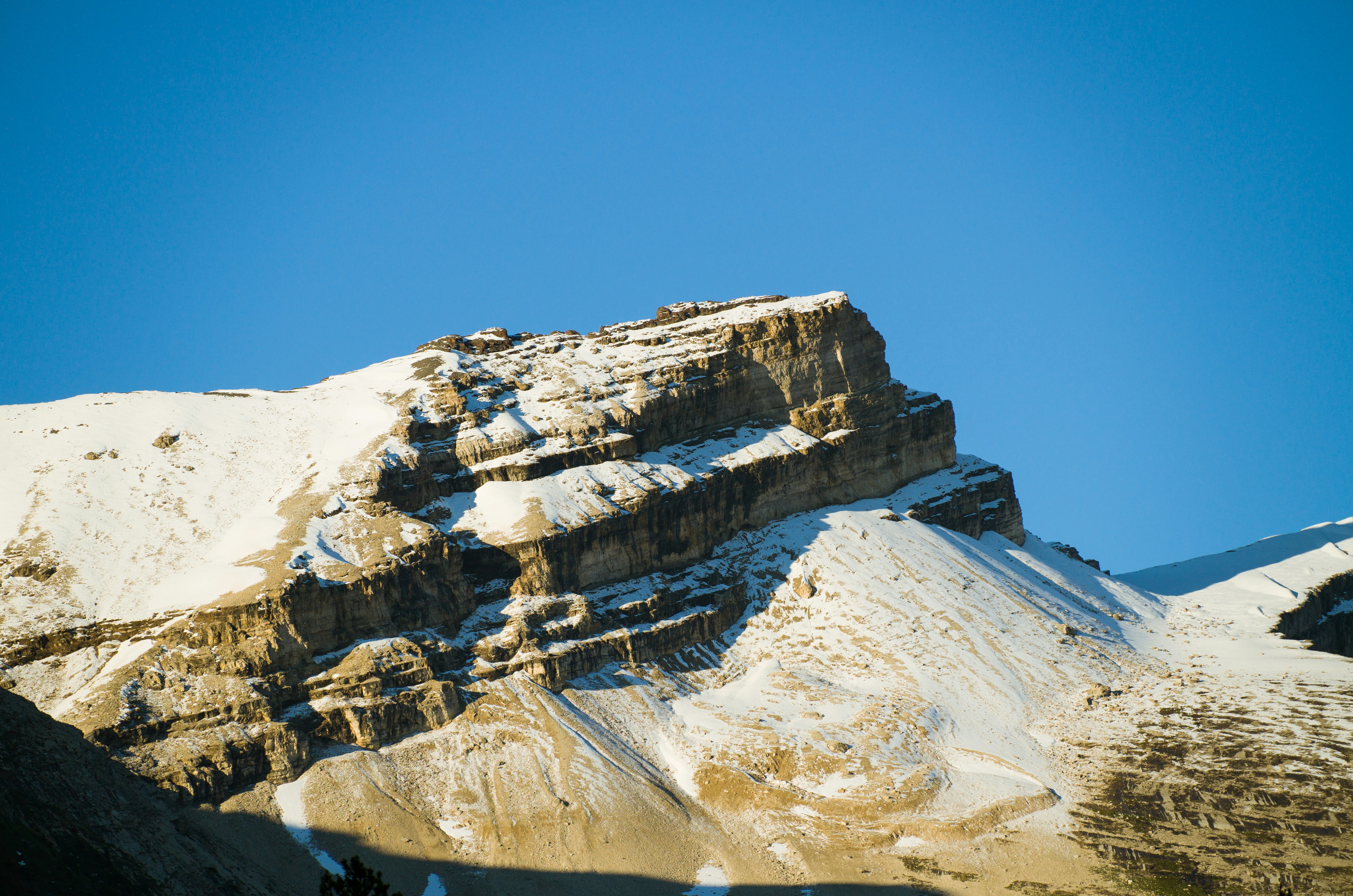 Rocky snow-dusted mountain ridge against a clear blue sky.