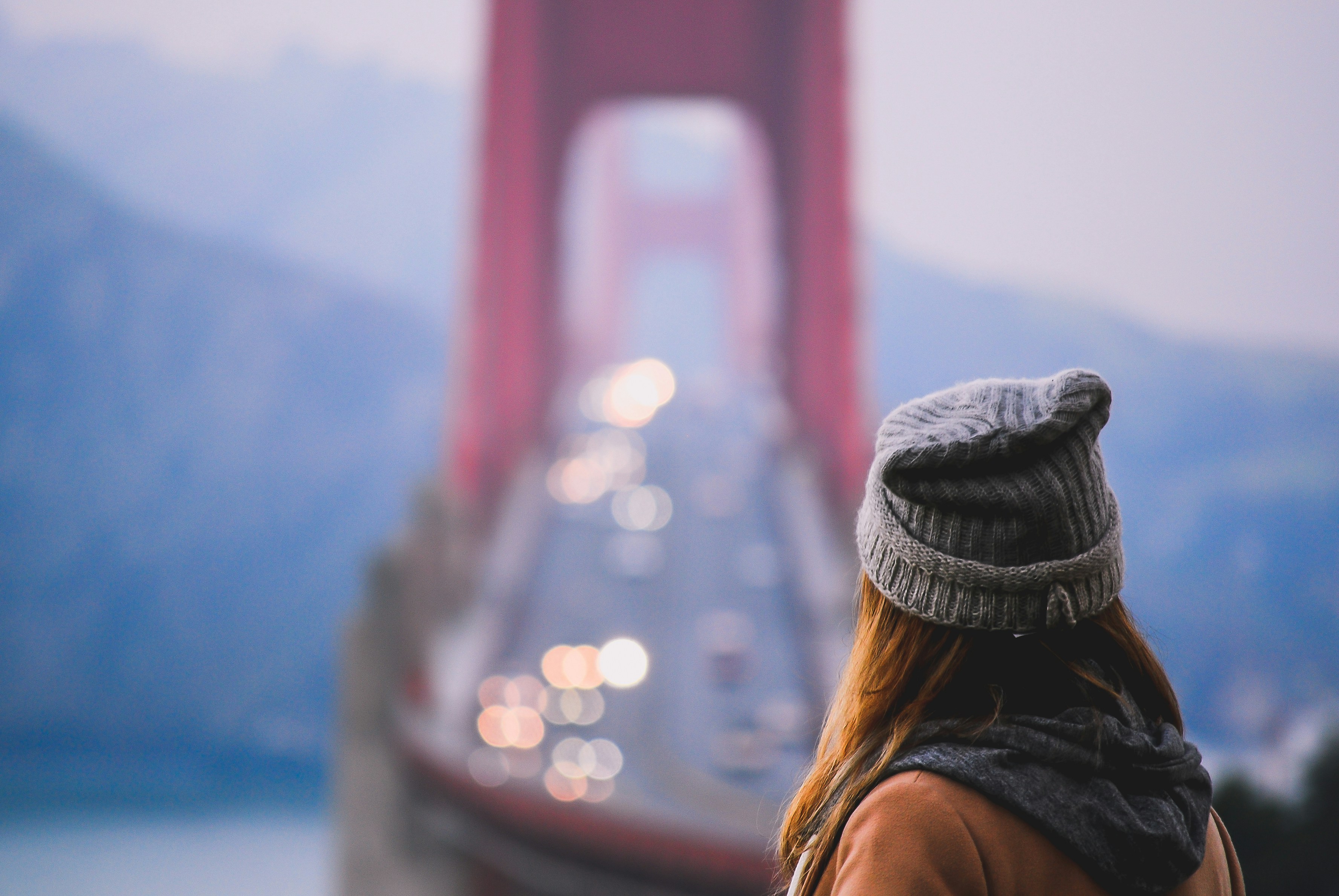 Person in gray knit hat gazing towards a large suspension bridge on a foggy day.