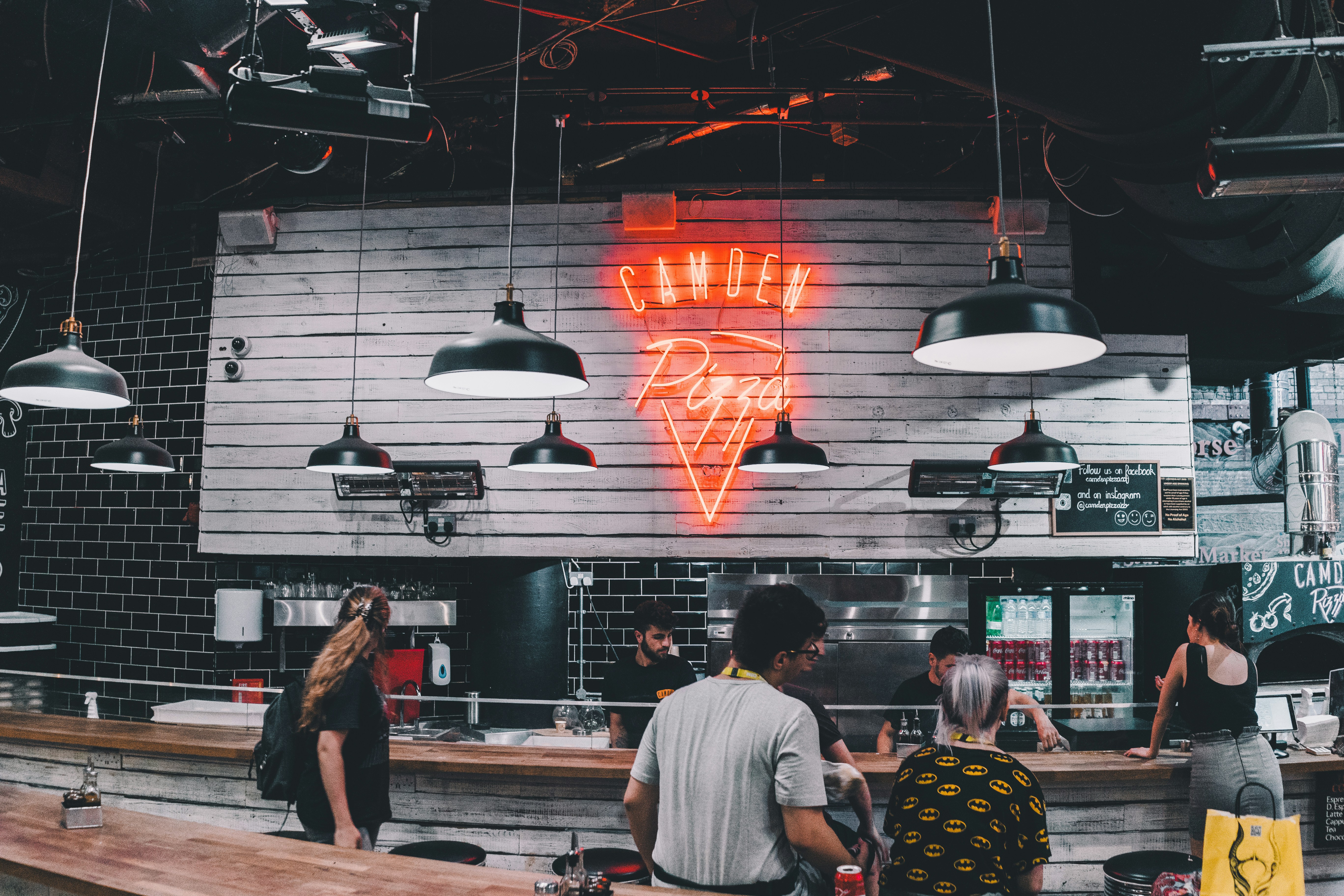 A lively pizza restaurant scene featuring a neon sign, modern decor, and patrons enjoying their meals at the bar.