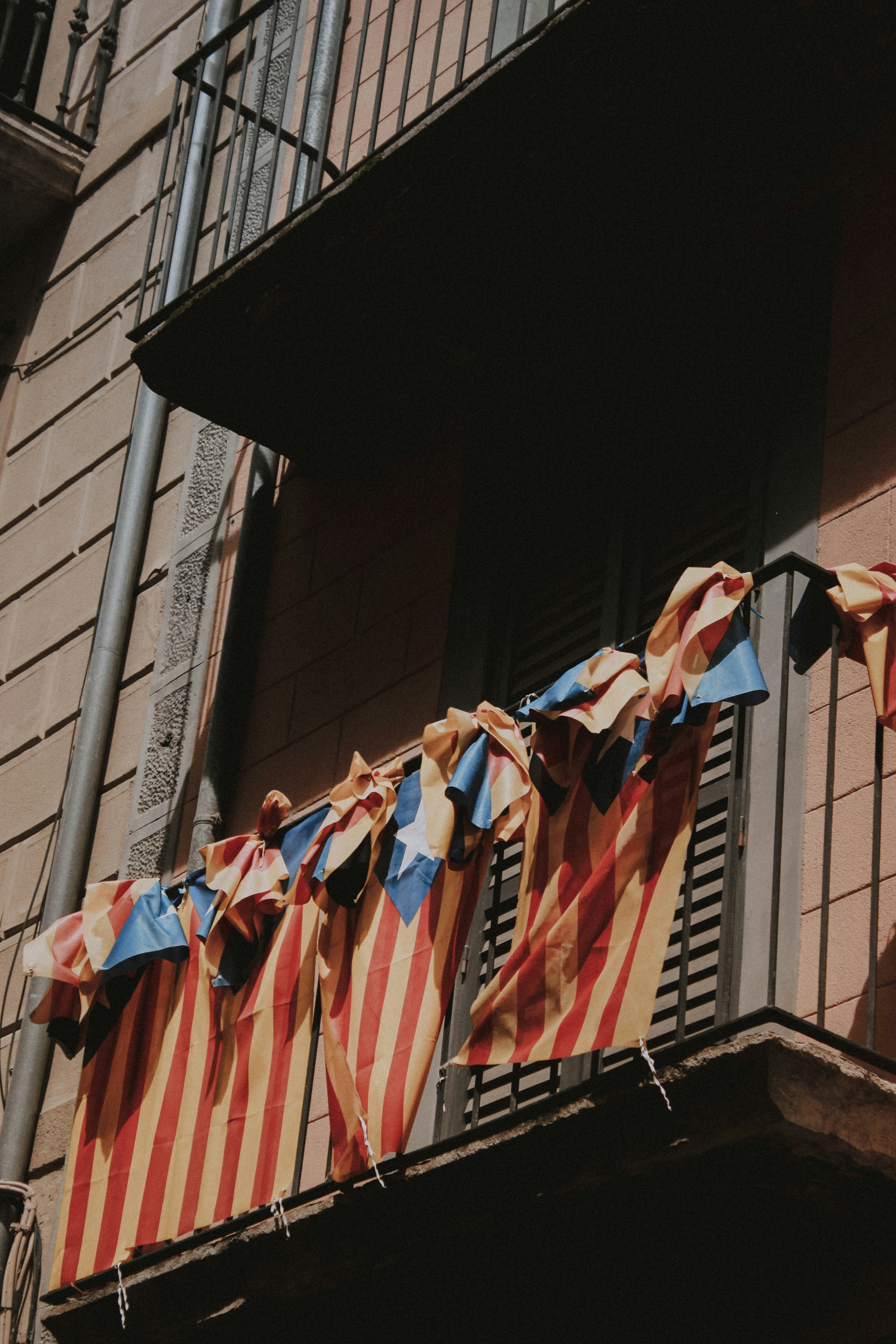 Catalan flags draped over a shaded balcony railing in a narrow street.