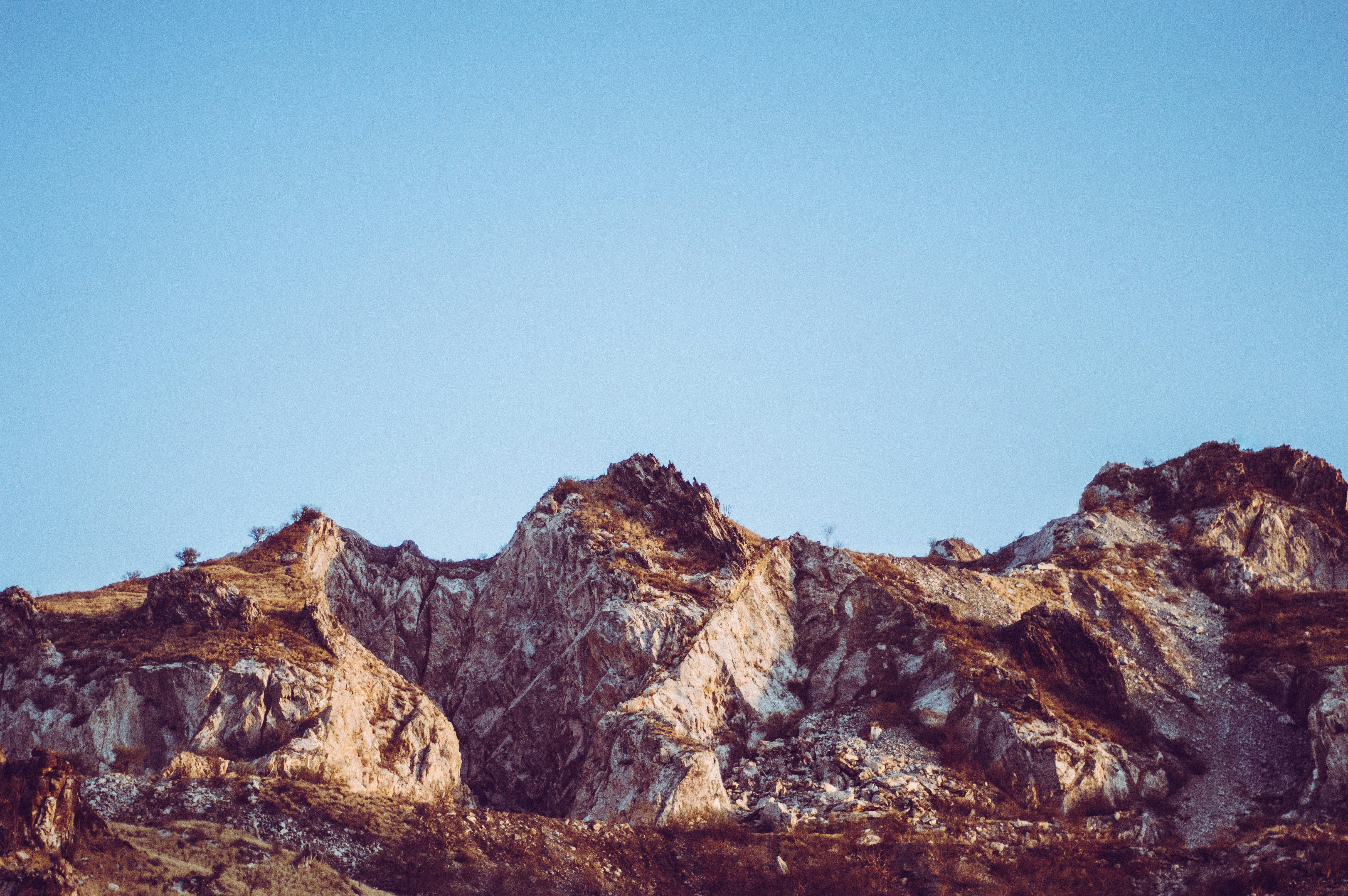 Rocky mountain range under a clear blue sky, bathed in warm sunset light.