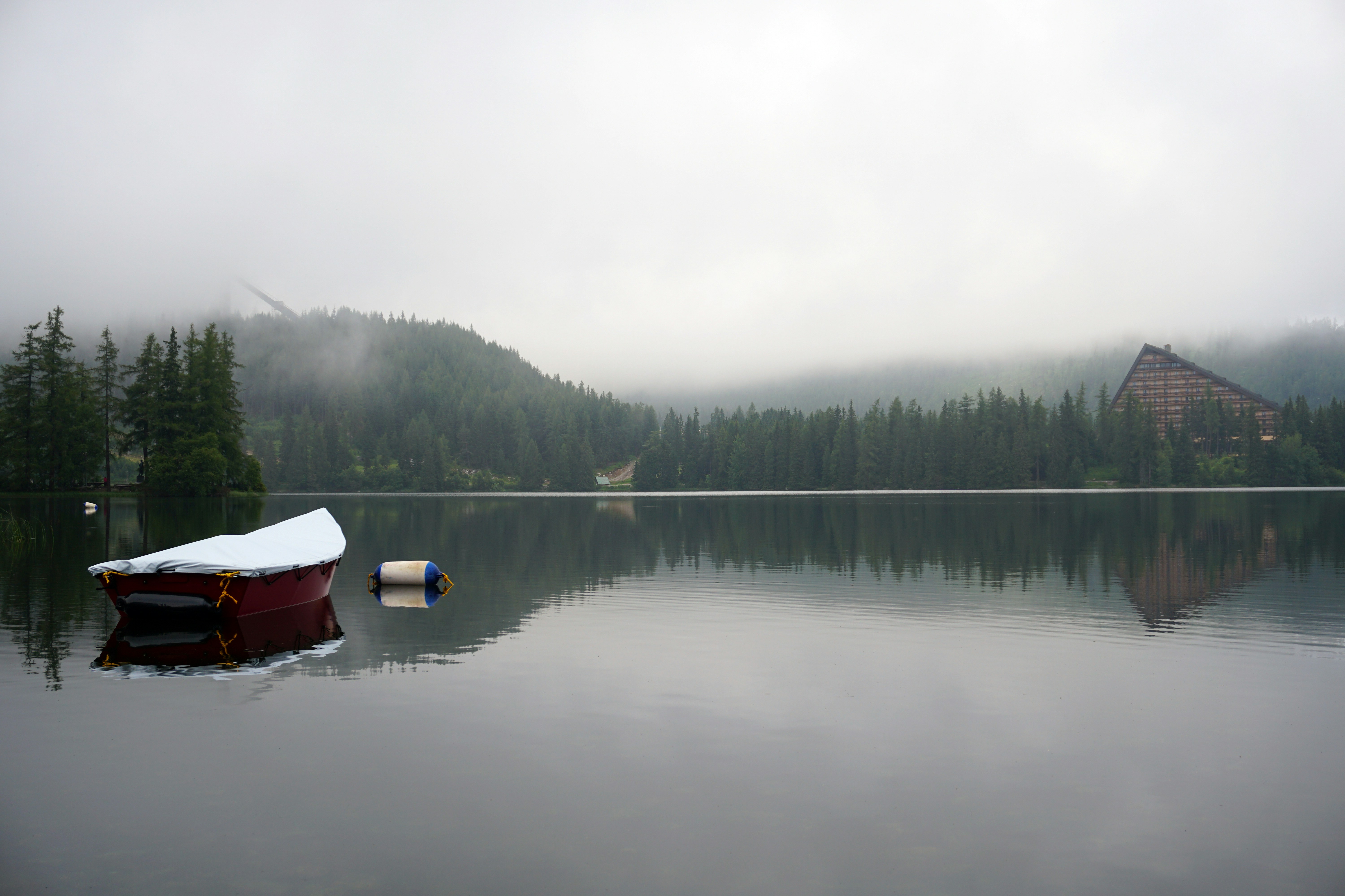 Lonely boat anchored on a mist-covered lake with a foggy forest backdrop.
