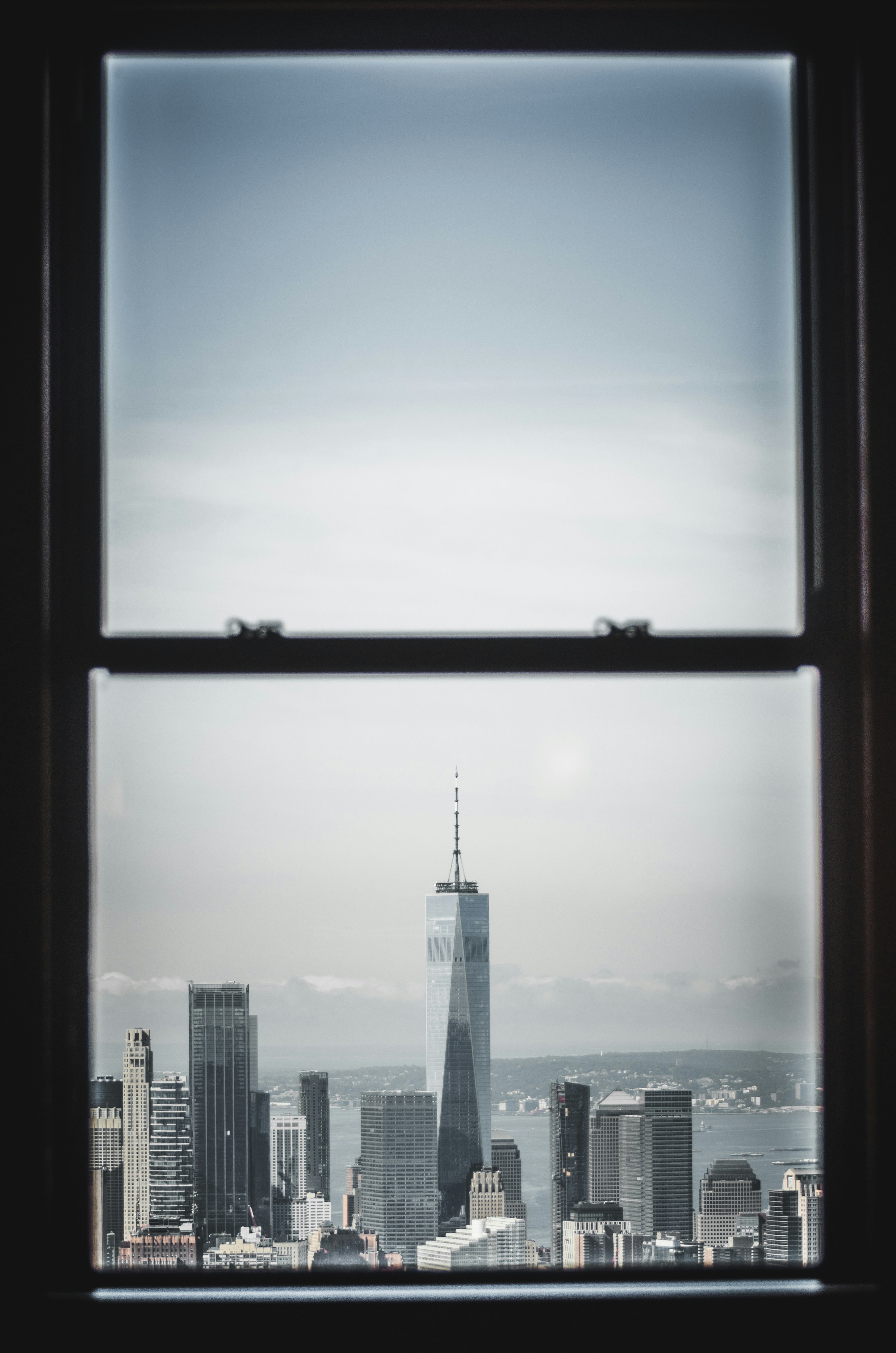 View of One World Trade Center framed by a window, showcasing the urban landscape of New York City. The scene captures the blend of architecture and sky.