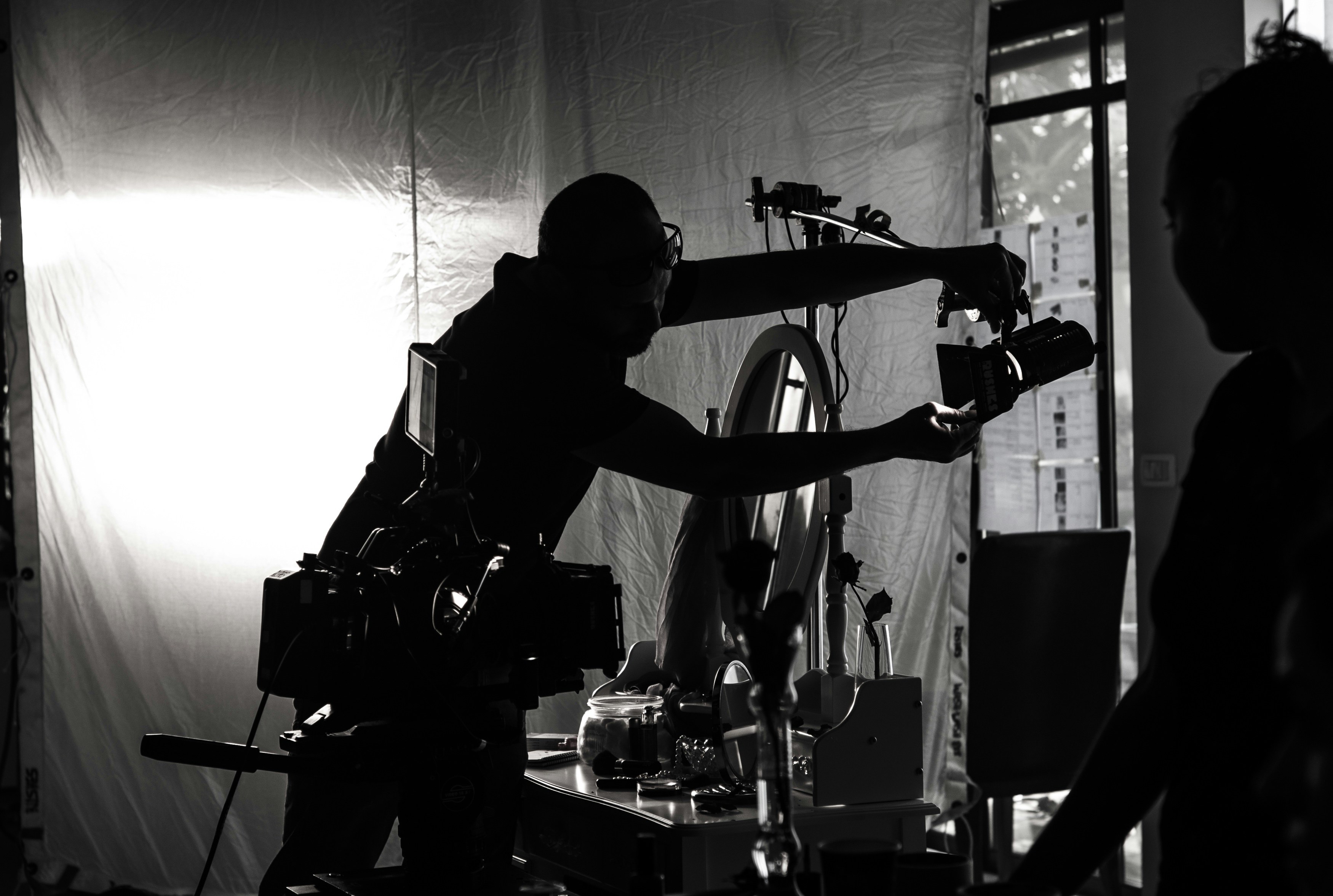 Silhouetted photographer adjusting equipment in a studio, surrounded by soft lighting and various props.