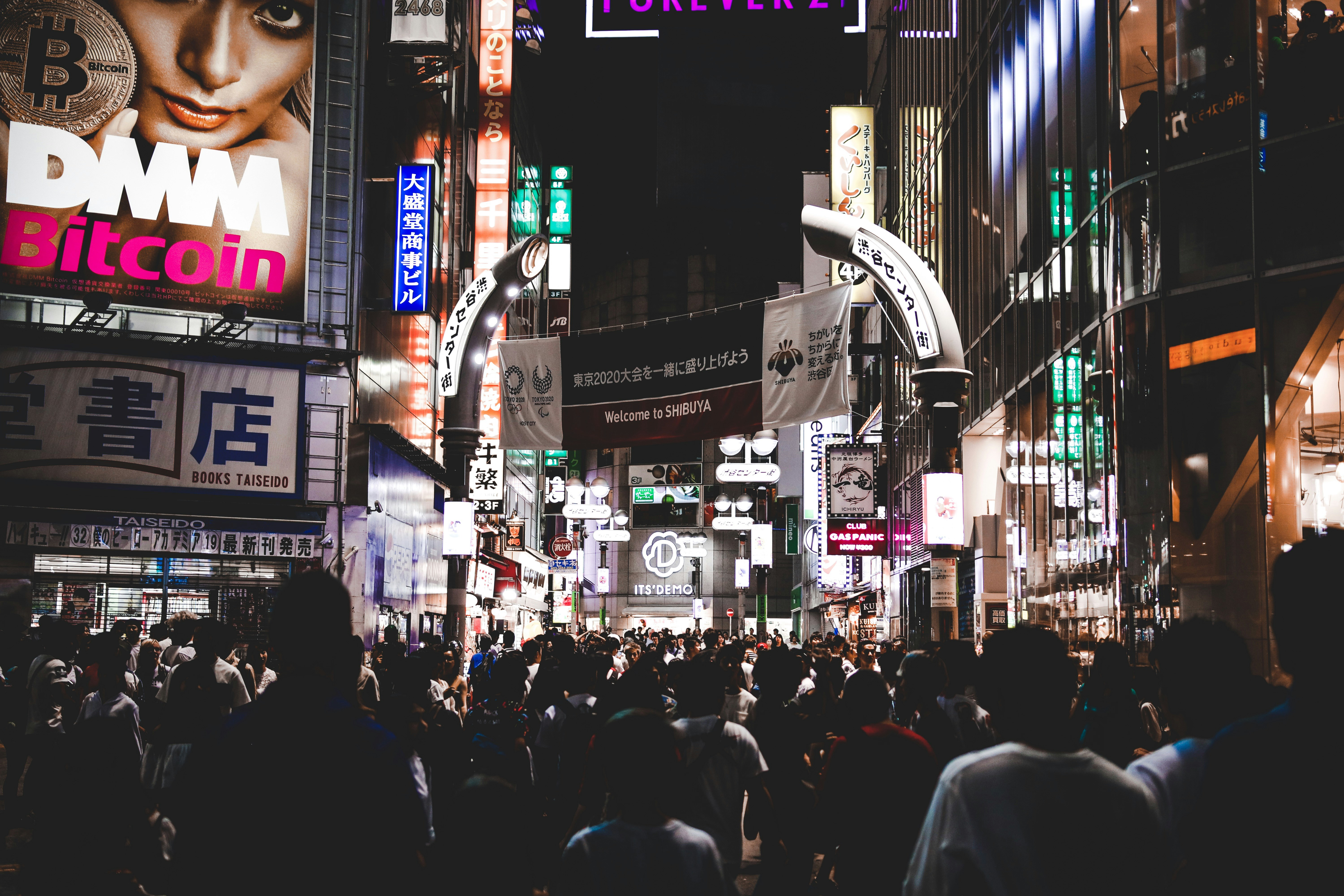 Crowd navigating through a vibrant urban street illuminated by neon signs and advertisements at night.