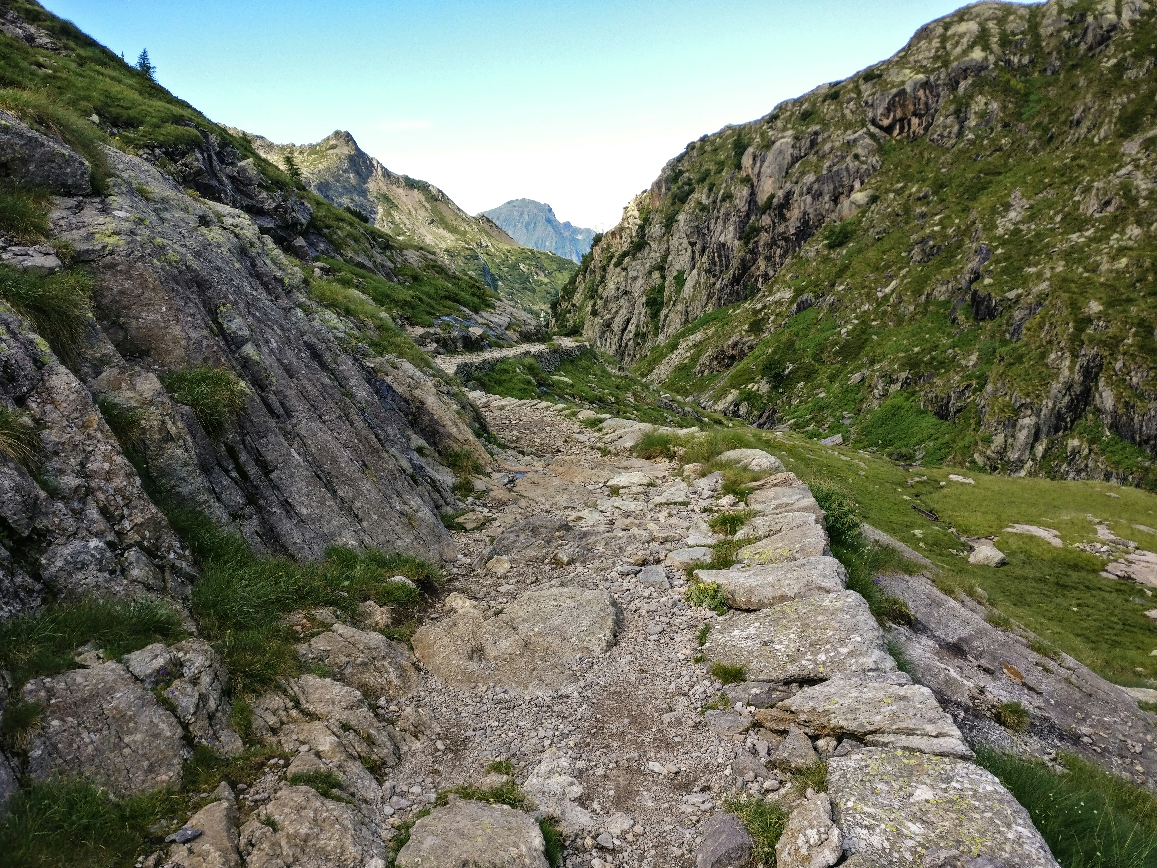 Stone pathway winding through rugged green mountains under a clear sky.