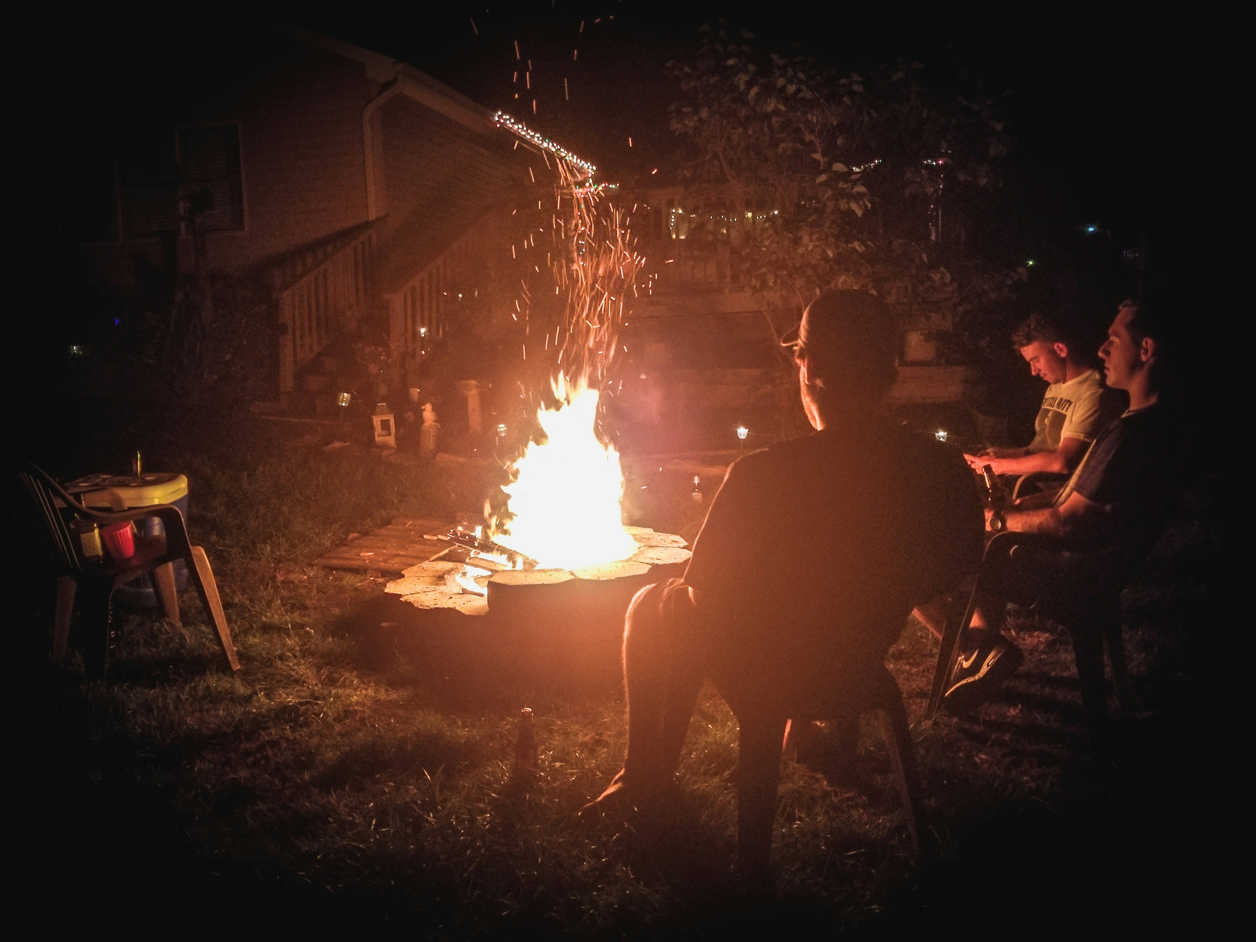 Three friends gathered around a roaring campfire, sharing stories as sparks dance into the night sky.