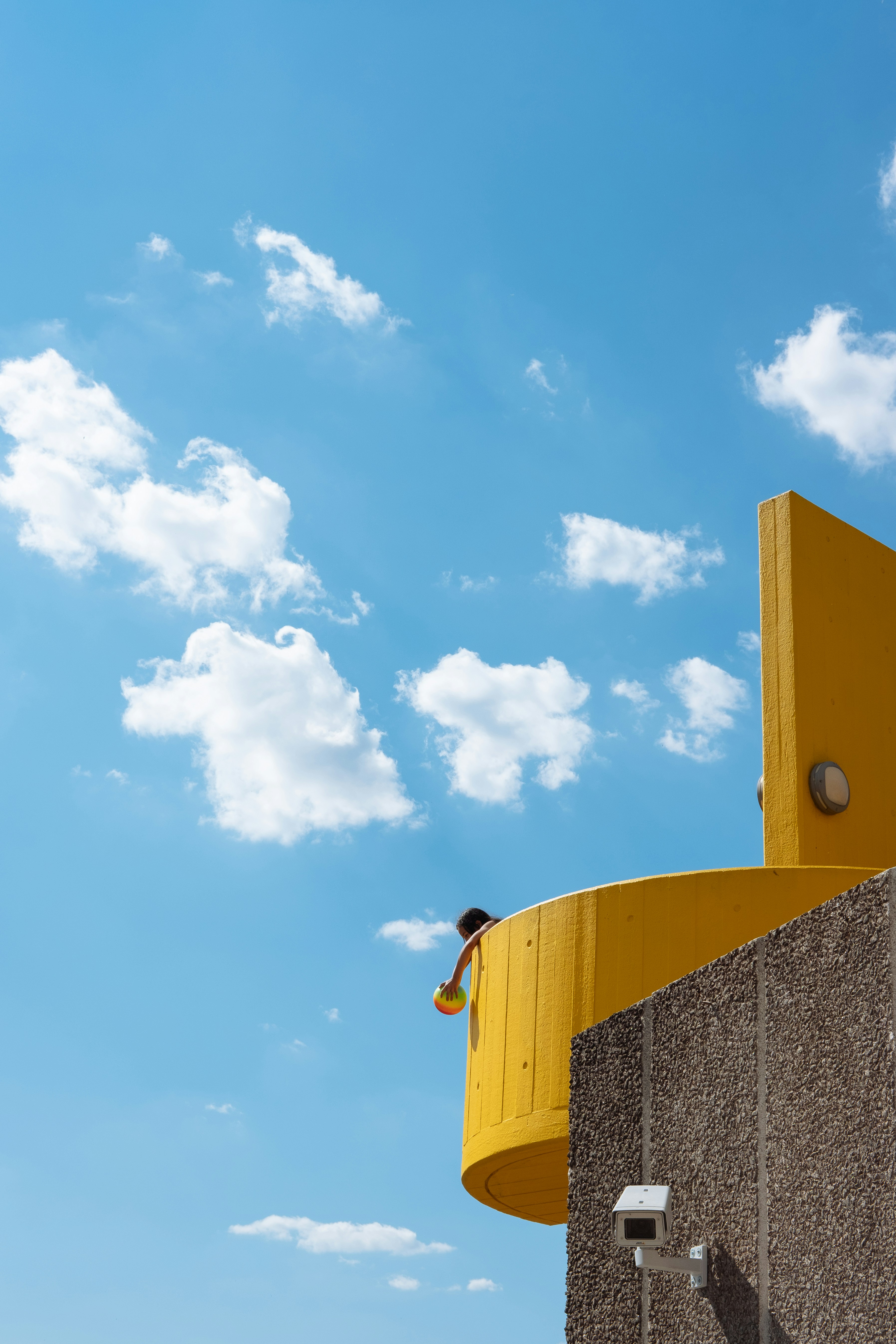 A vibrant yellow architectural element contrasts against a clear blue sky dotted with fluffy clouds.