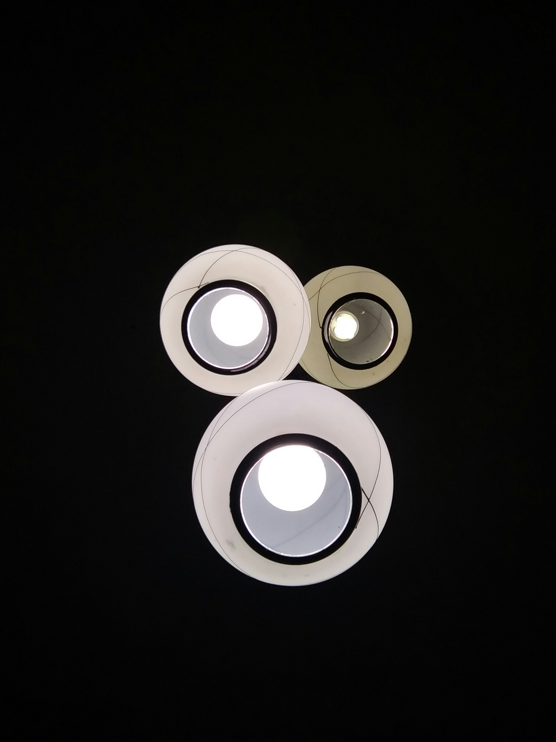 Three circular light fixtures arranged in a triangle against a black background, creating a minimalist, geometric composition.