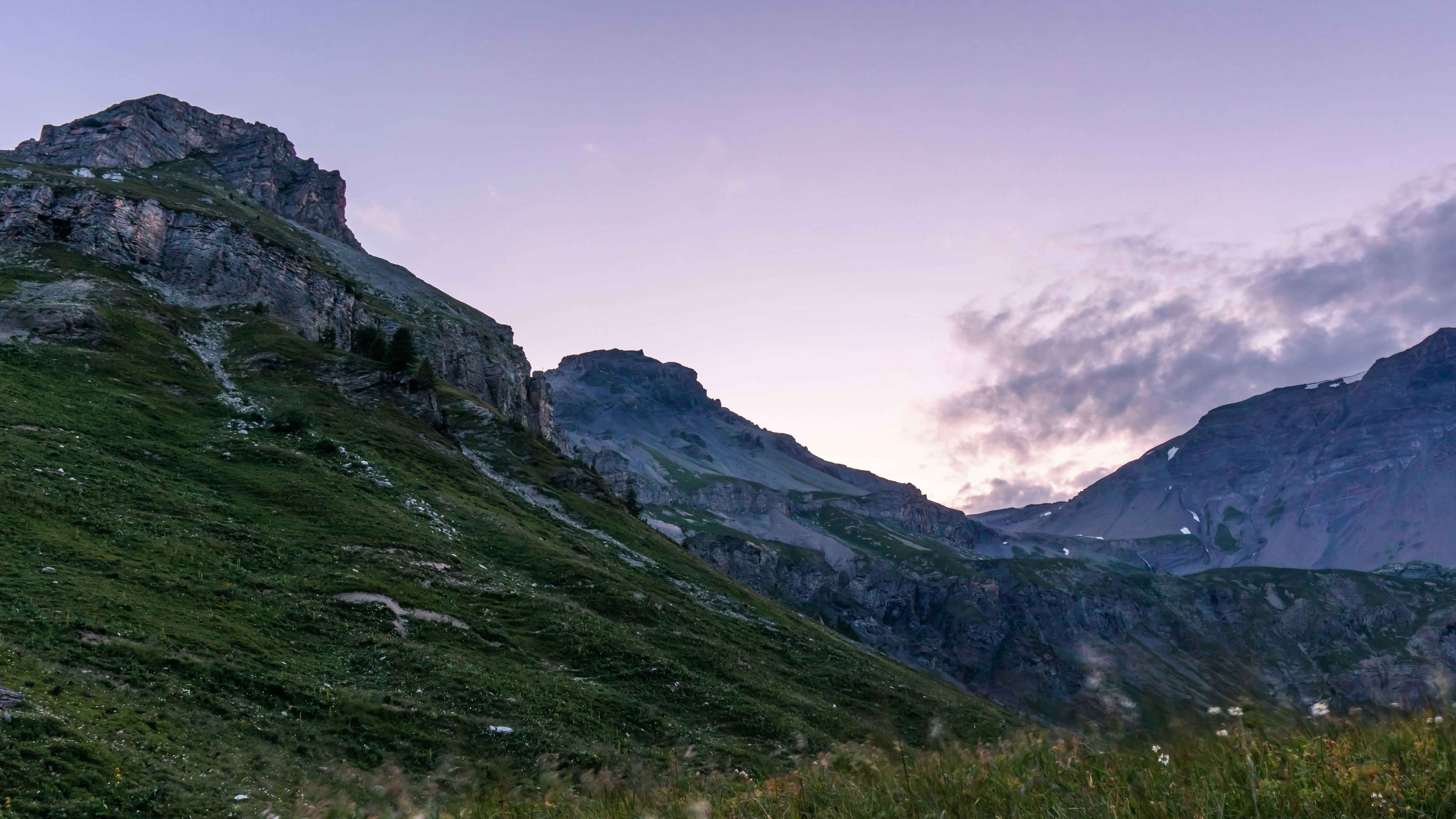 Sunset light fades over rugged mountain slopes with a clear sky and scattered clouds.